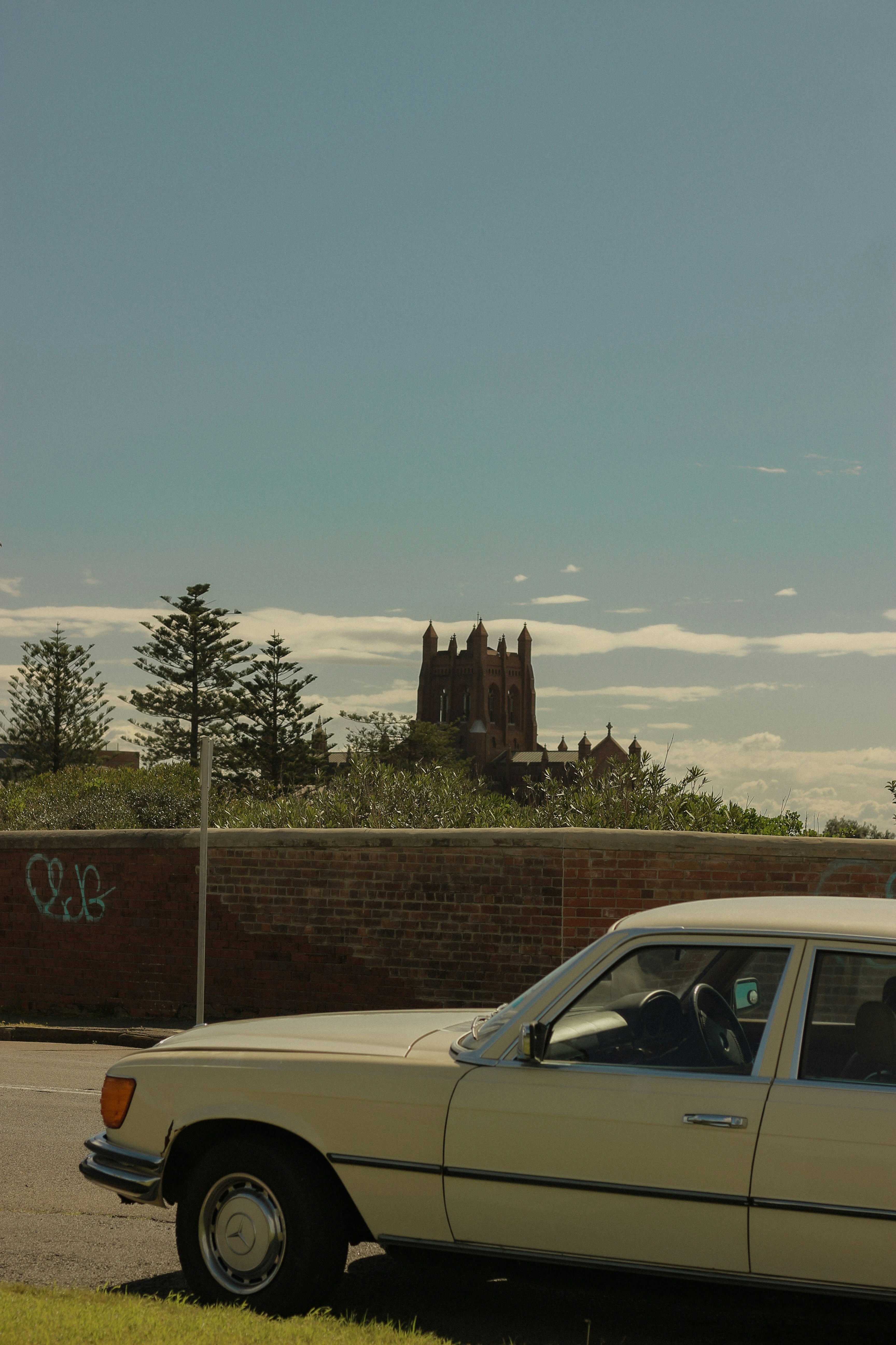 Vintage sedan at the edge of town with a distant cathedral rising above a brick wall