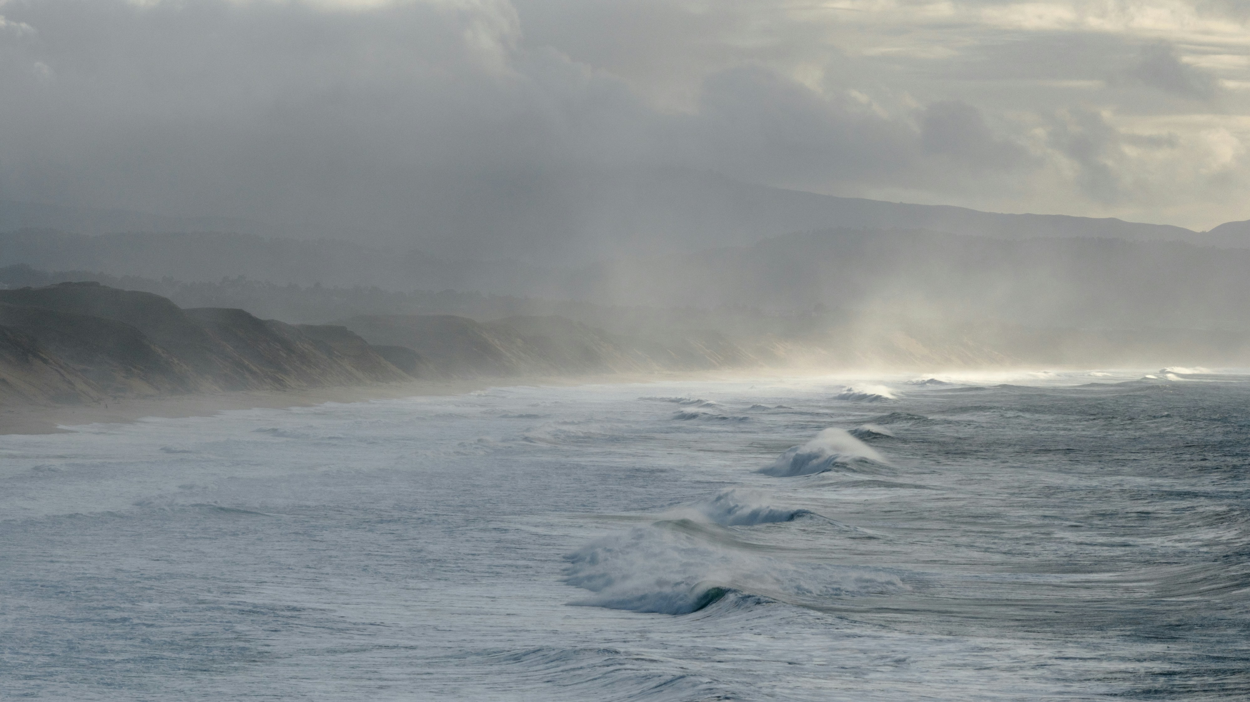 Mist hangs over a sunlit beach in Monterey, California, with a line of waves rolling in.