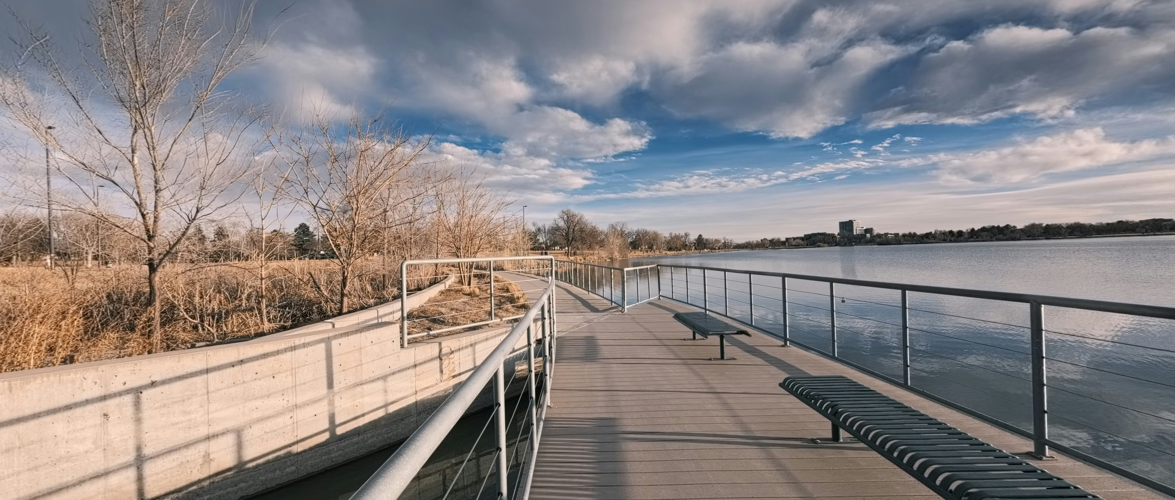 Boardwalk along a lake with benches and cloudy sky