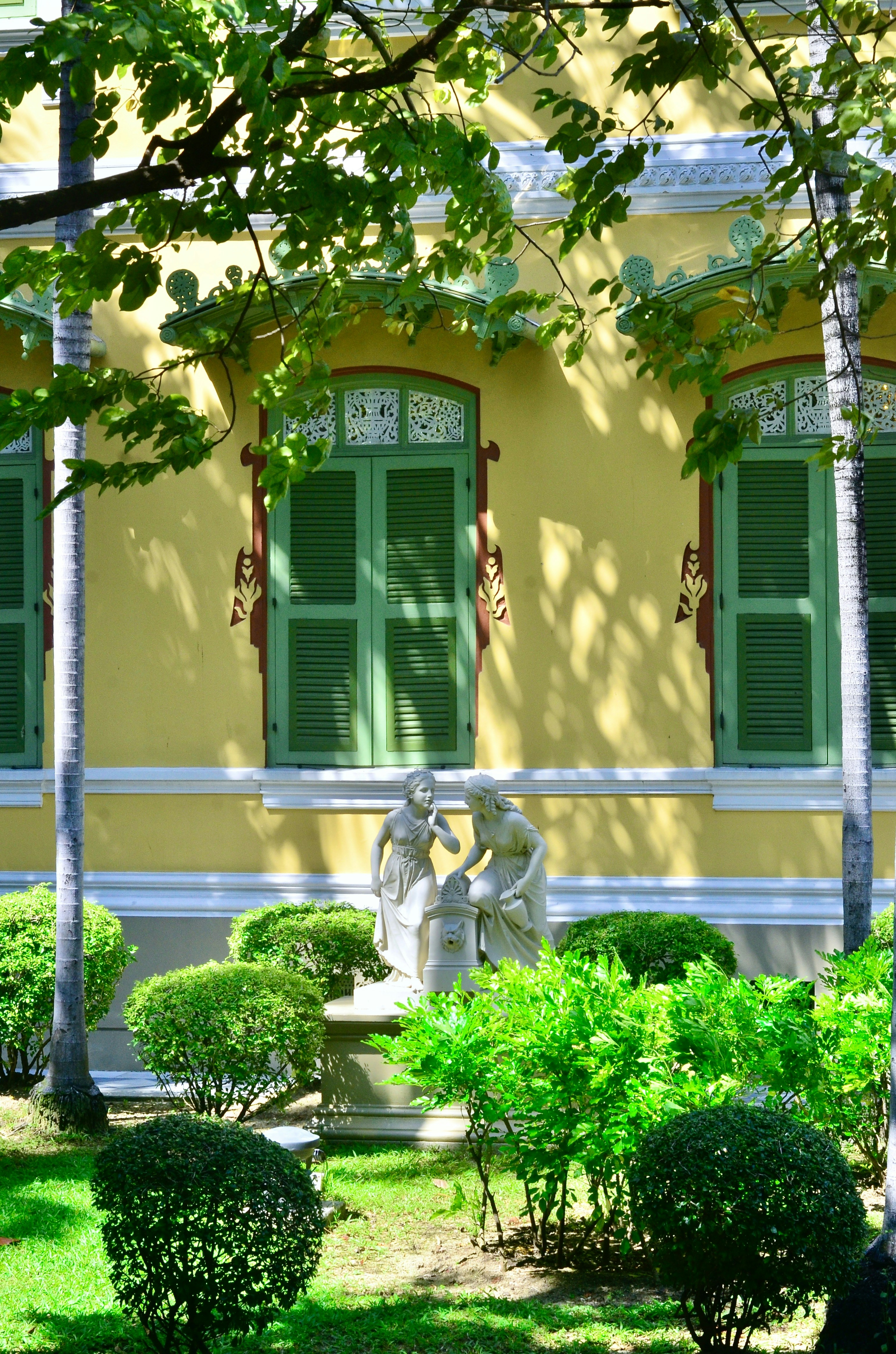 Sunlit Yellow Villa Framed by Green Foliage and a Classical Garden Sculpture