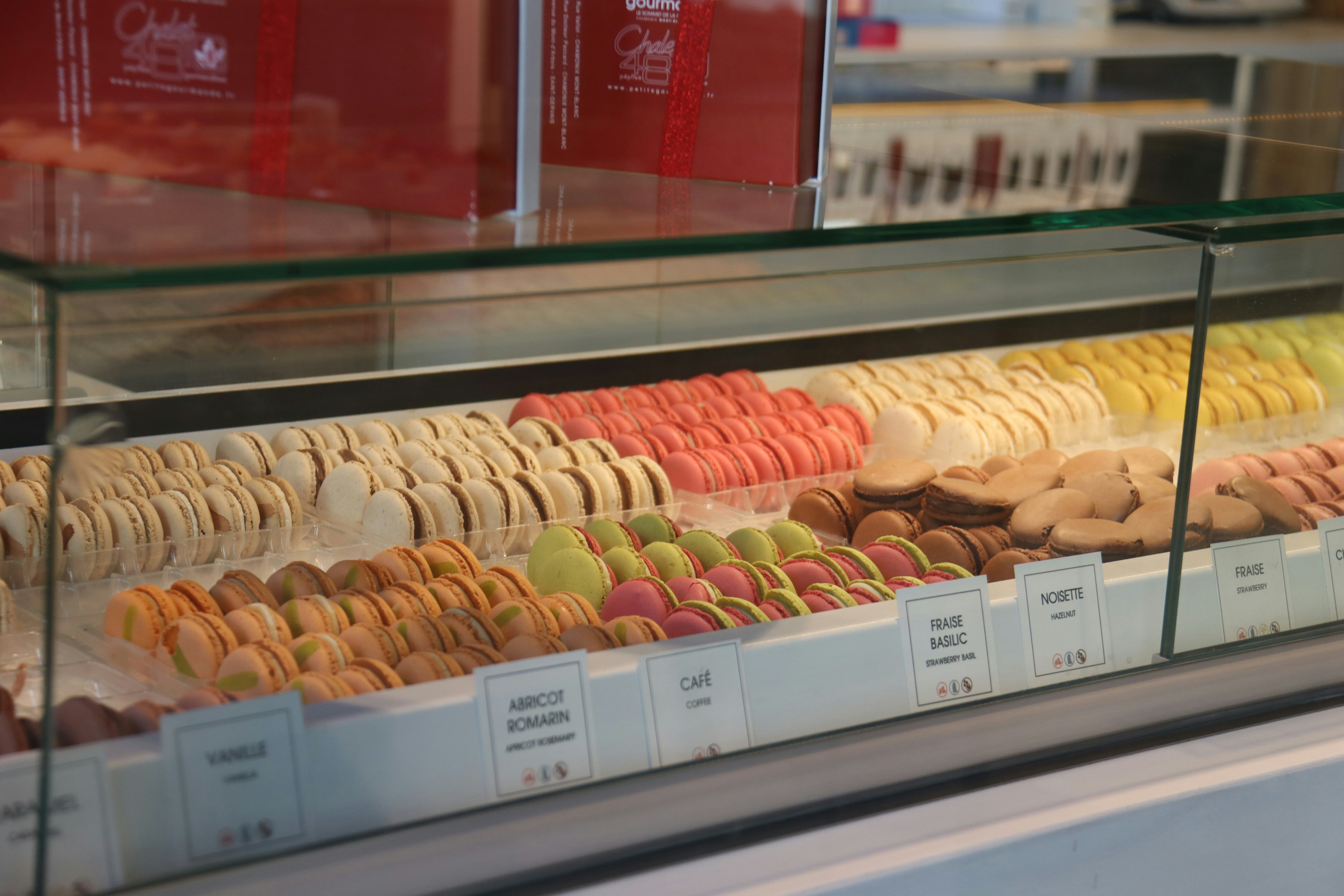 Row of pastel macarons glows behind curved glass in a cozy bakery display