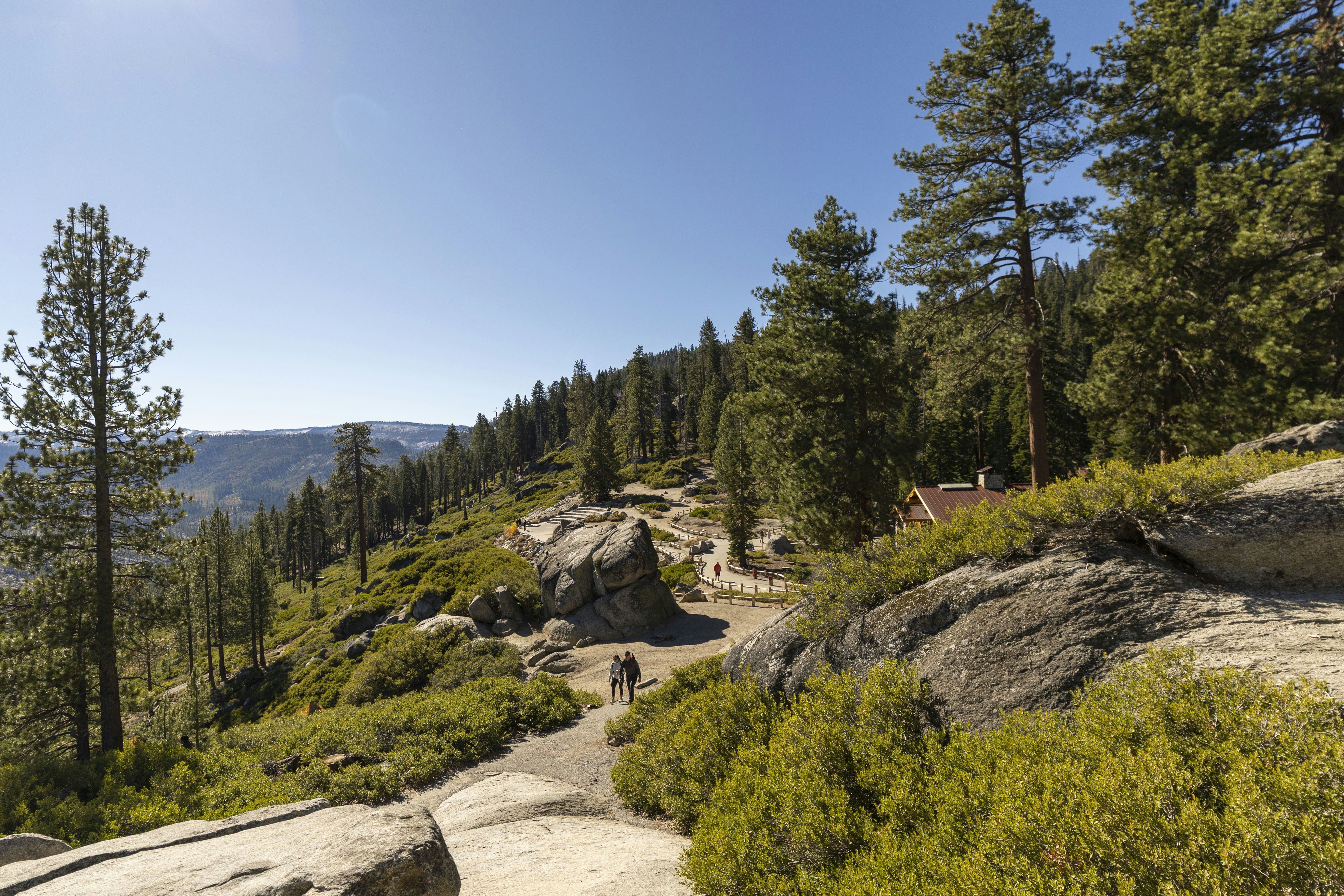 Hikers on a trail through a rocky, forested landscape.