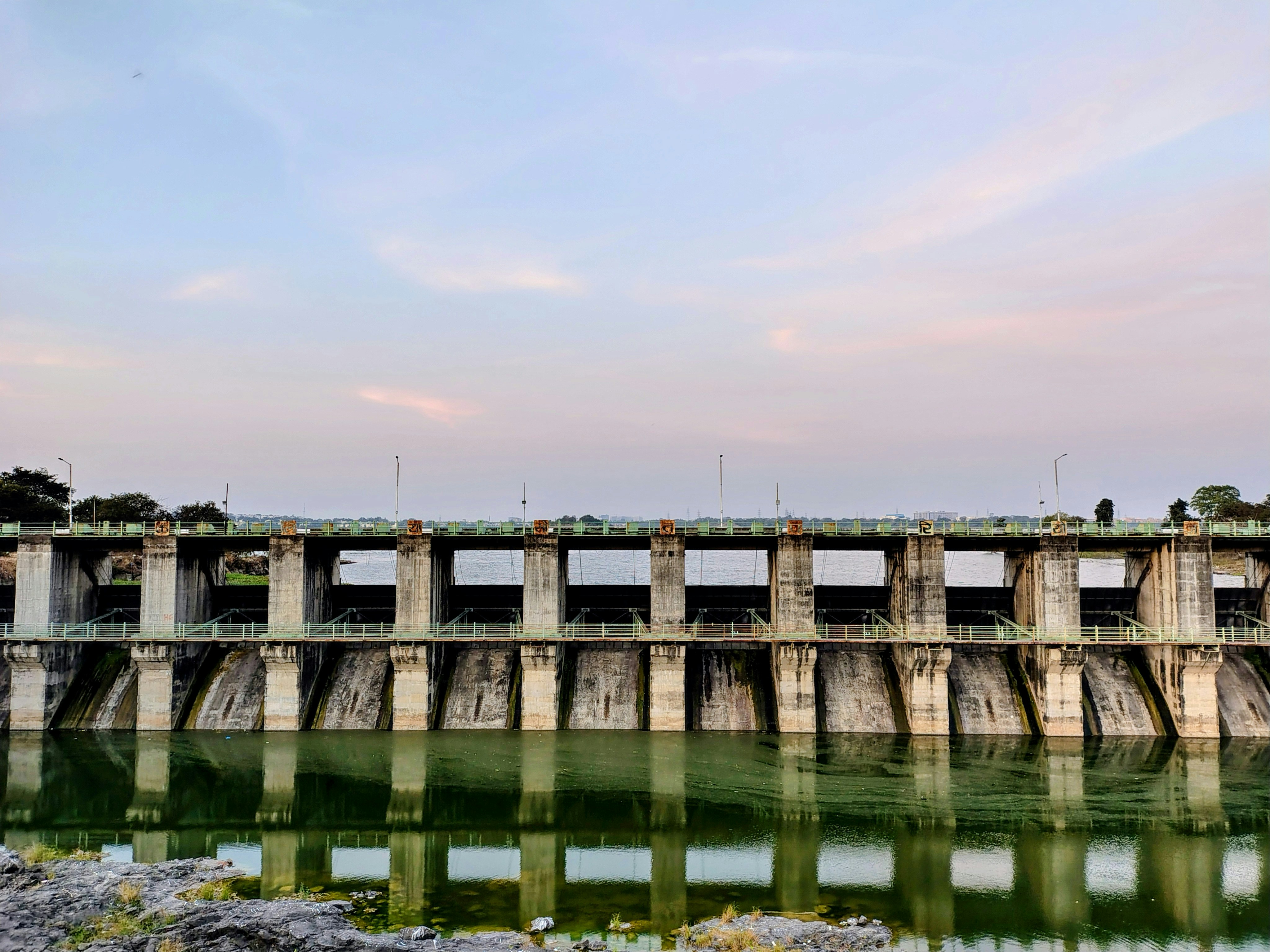 A serene view of Kaliyasot Dam in Bhopal, Madhya Pradesh, captured during a calm evening with soft pastel skies reflected on the water. This scenic dam is an important water reservoir and a popular spot for nature lovers, photographers, and travelers exploring central India. The image highlights the peaceful blend of engineering and nature, making it ideal for travel, landscape, environment, and infrastructure-related visuals.