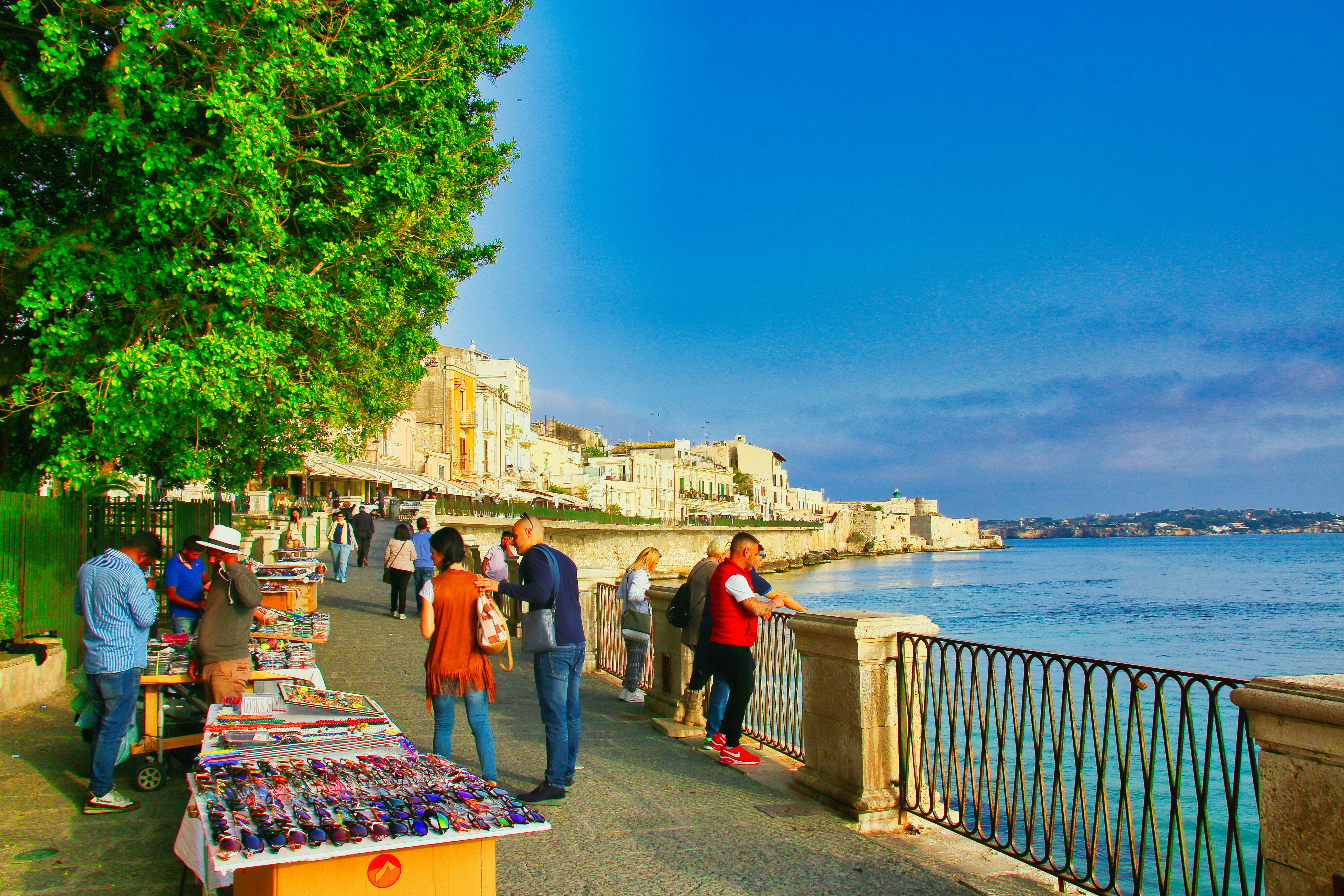 Sur la façade ouest de l’île d’Ortigia (Syracuse, en Sicile), la promenade d’Aréthuse offre un parcours piéton paisible entre mer, terrasses et horizons ouverts sur le soleil couchant.
