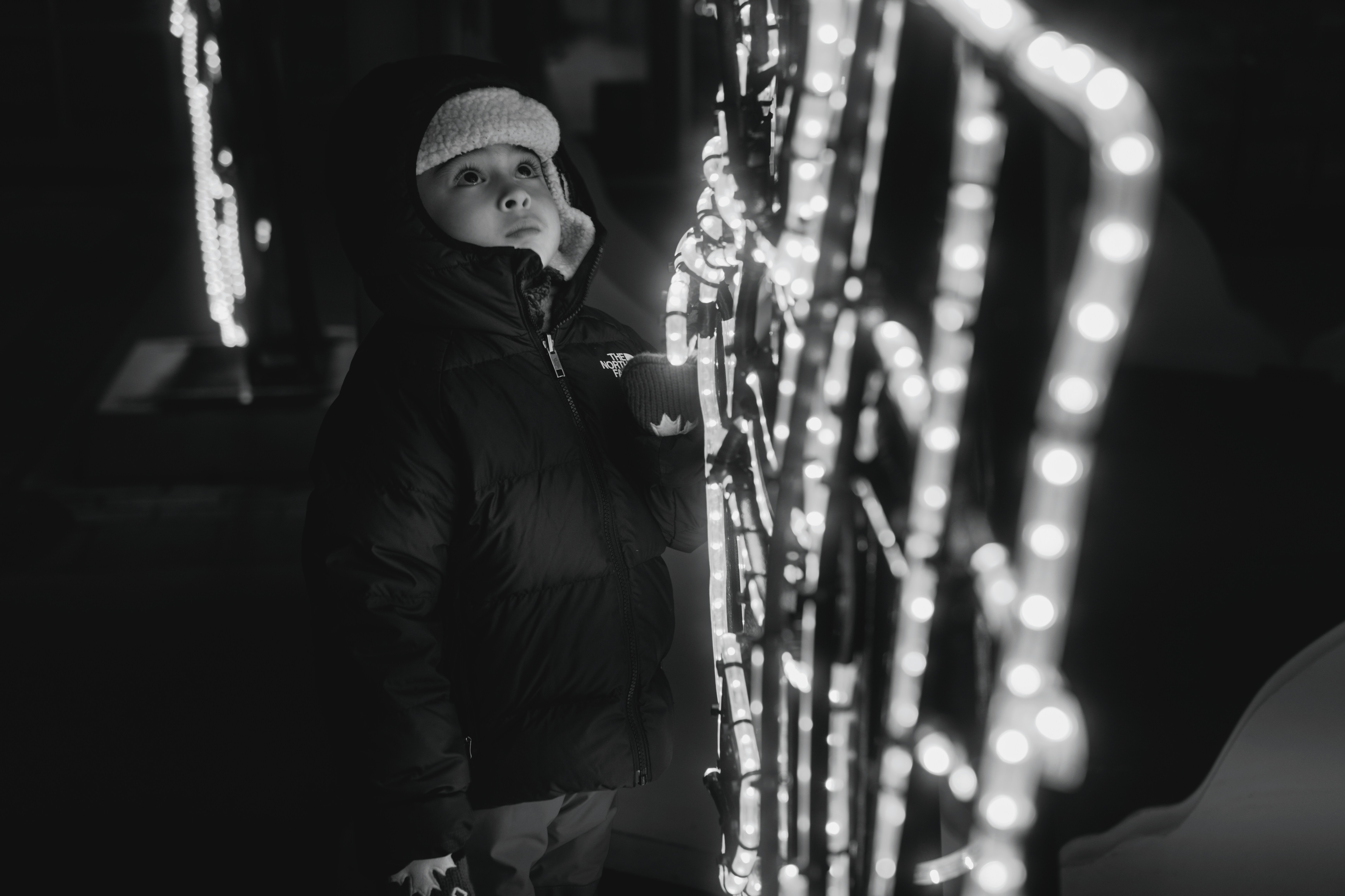 Child under illuminated winter lights: quiet curiosity in a darkened scene