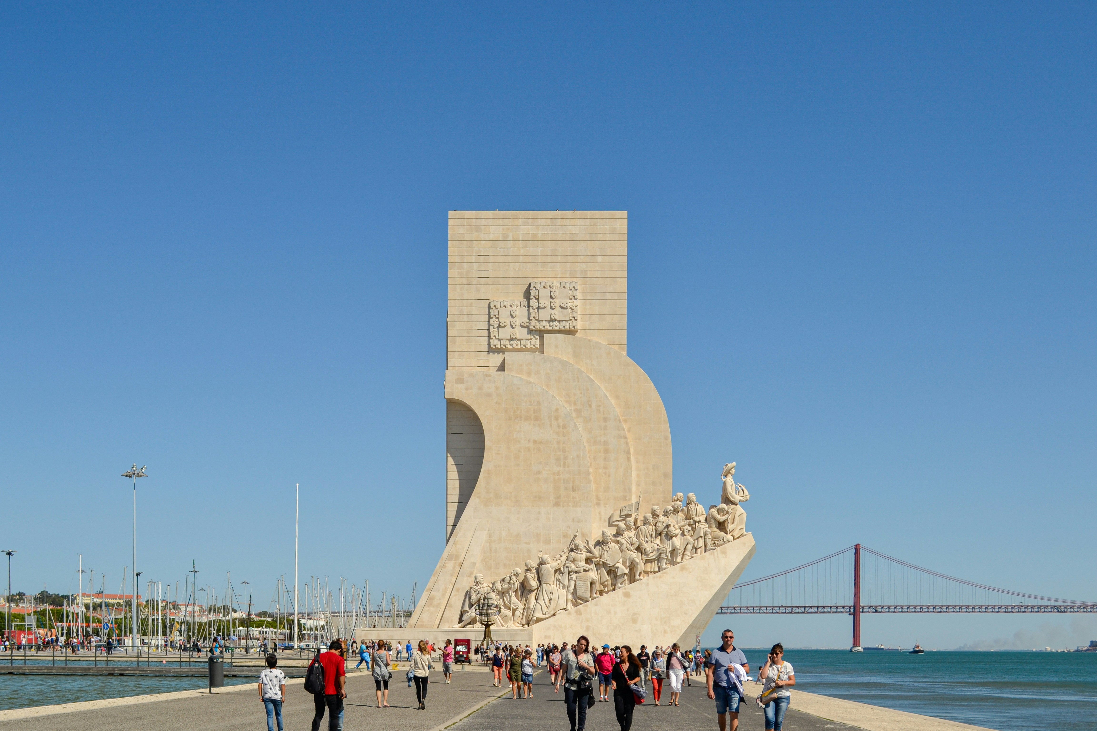 Monumental Staircase: People Walk the Pier Toward a Rising Stone Spiral
