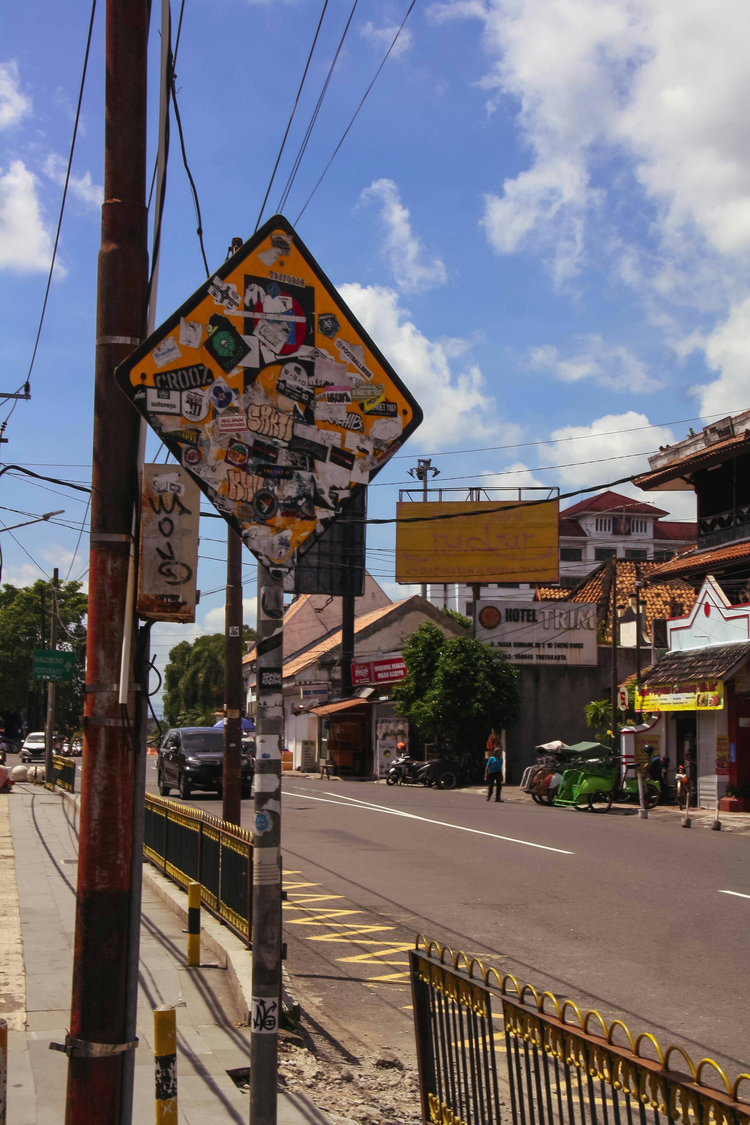 Stickered Road Sign in a Sunny Street Corridor