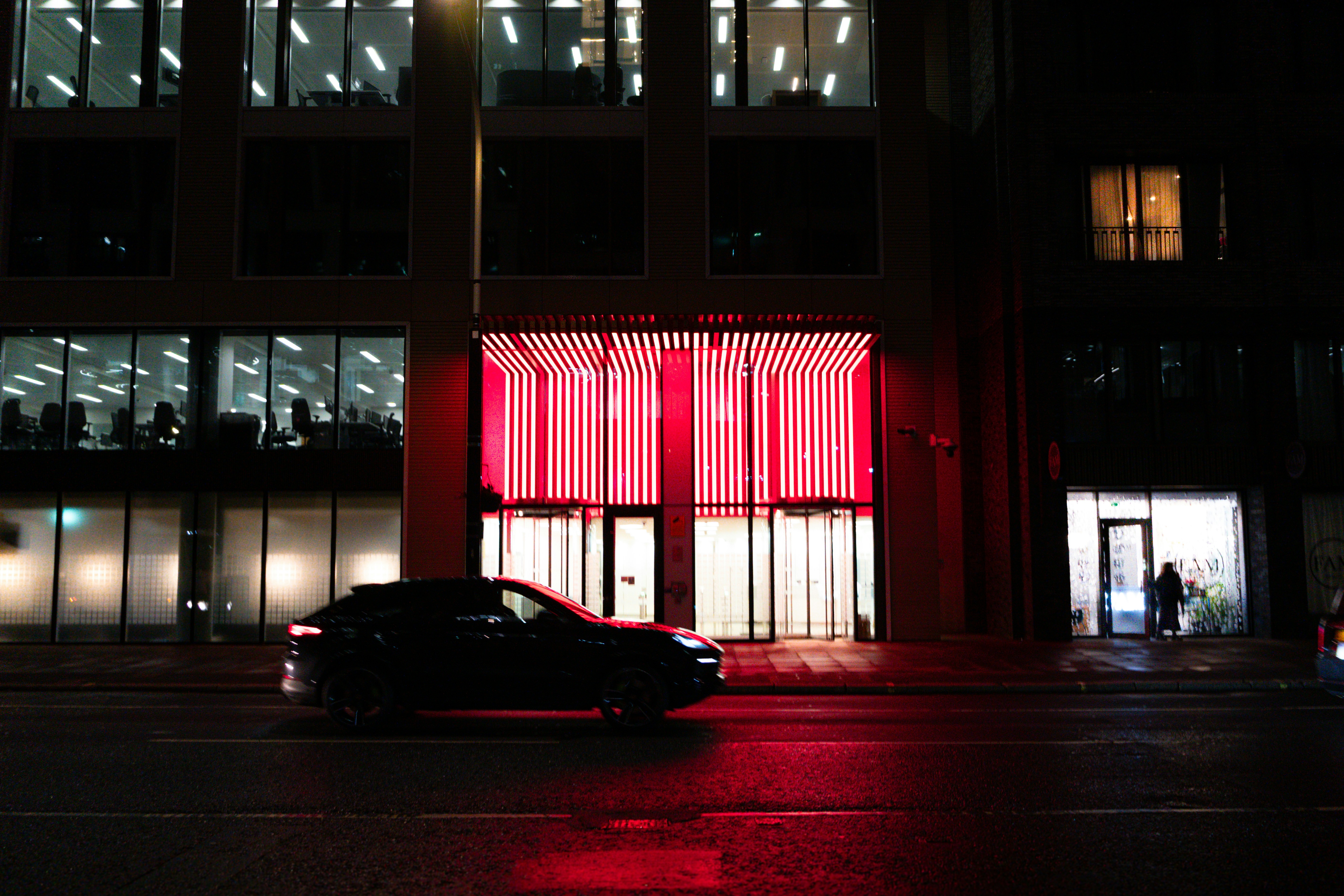 Neon-lit storefront and passing car on a rainy city night