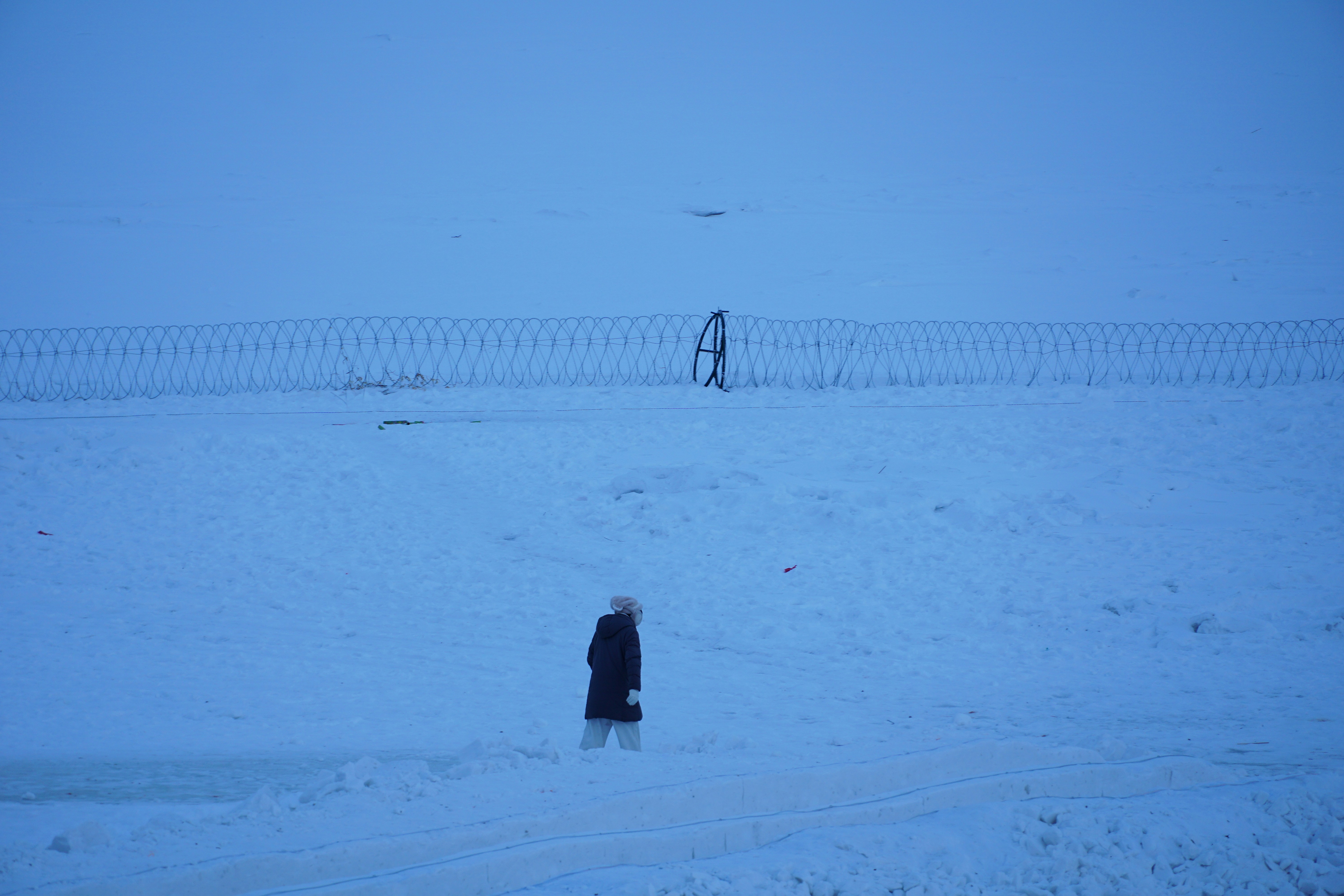  solitary figure in a blue winter field near a walled boundary