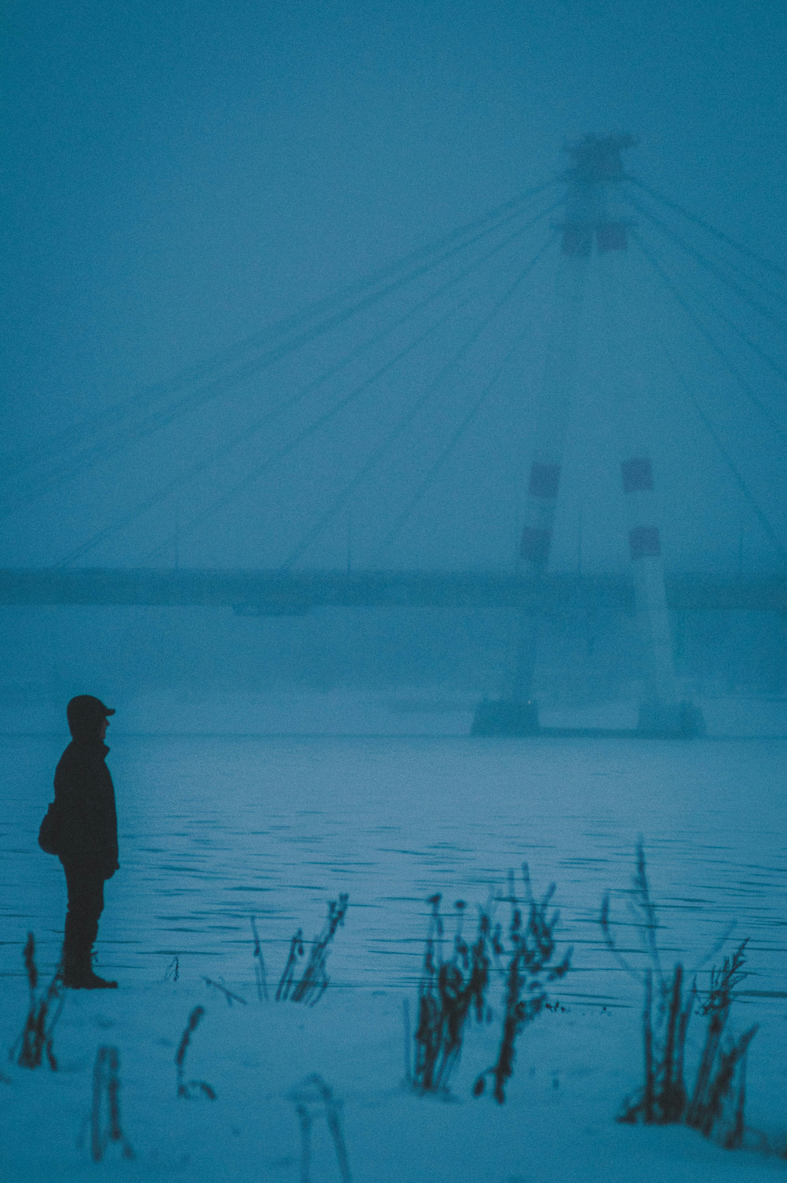 Silhouette of person by frozen river near bridge