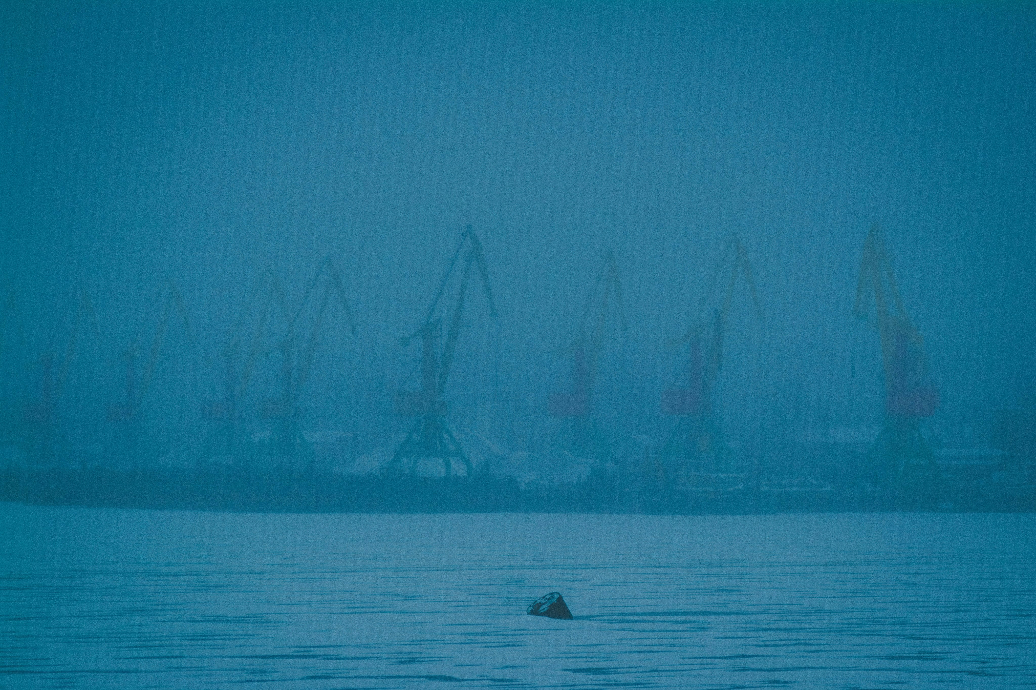 Industrial cranes in fog over frozen water