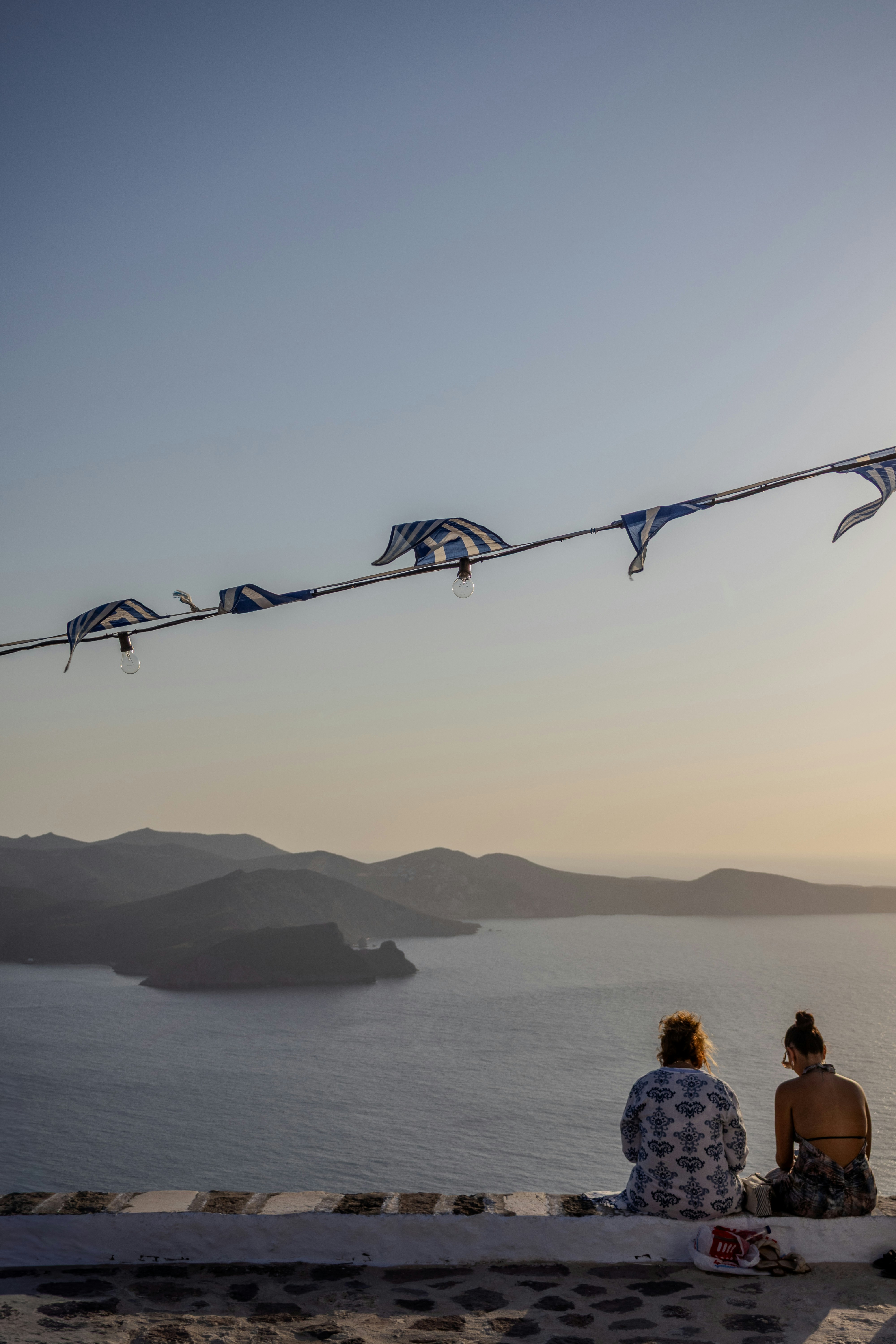 Sunset Embrace: Two Figures on a Cliff Overlooking Aegean Light