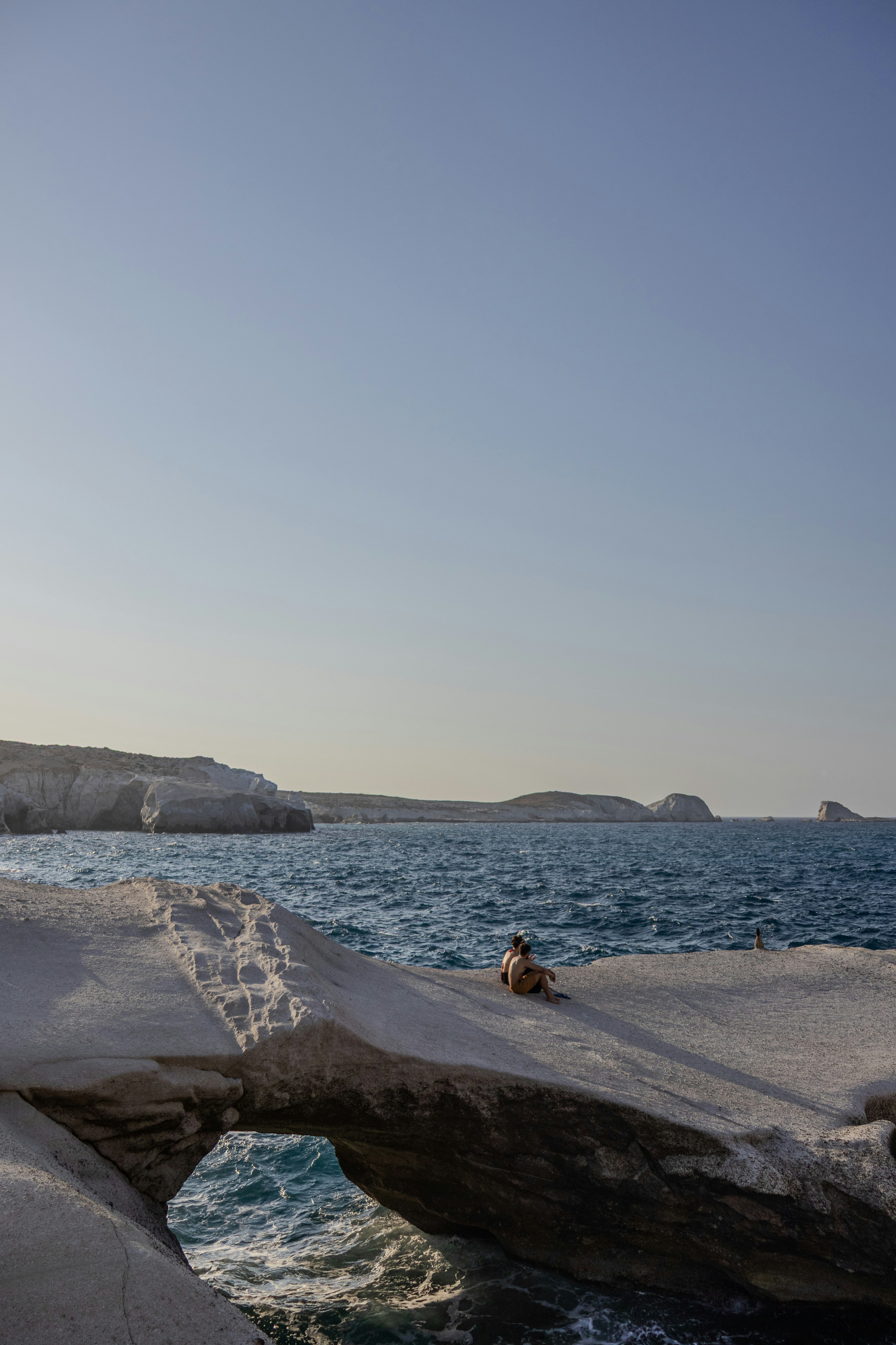 A person sits on a rock formation by the sea. photo – Free Sea Image on ...
