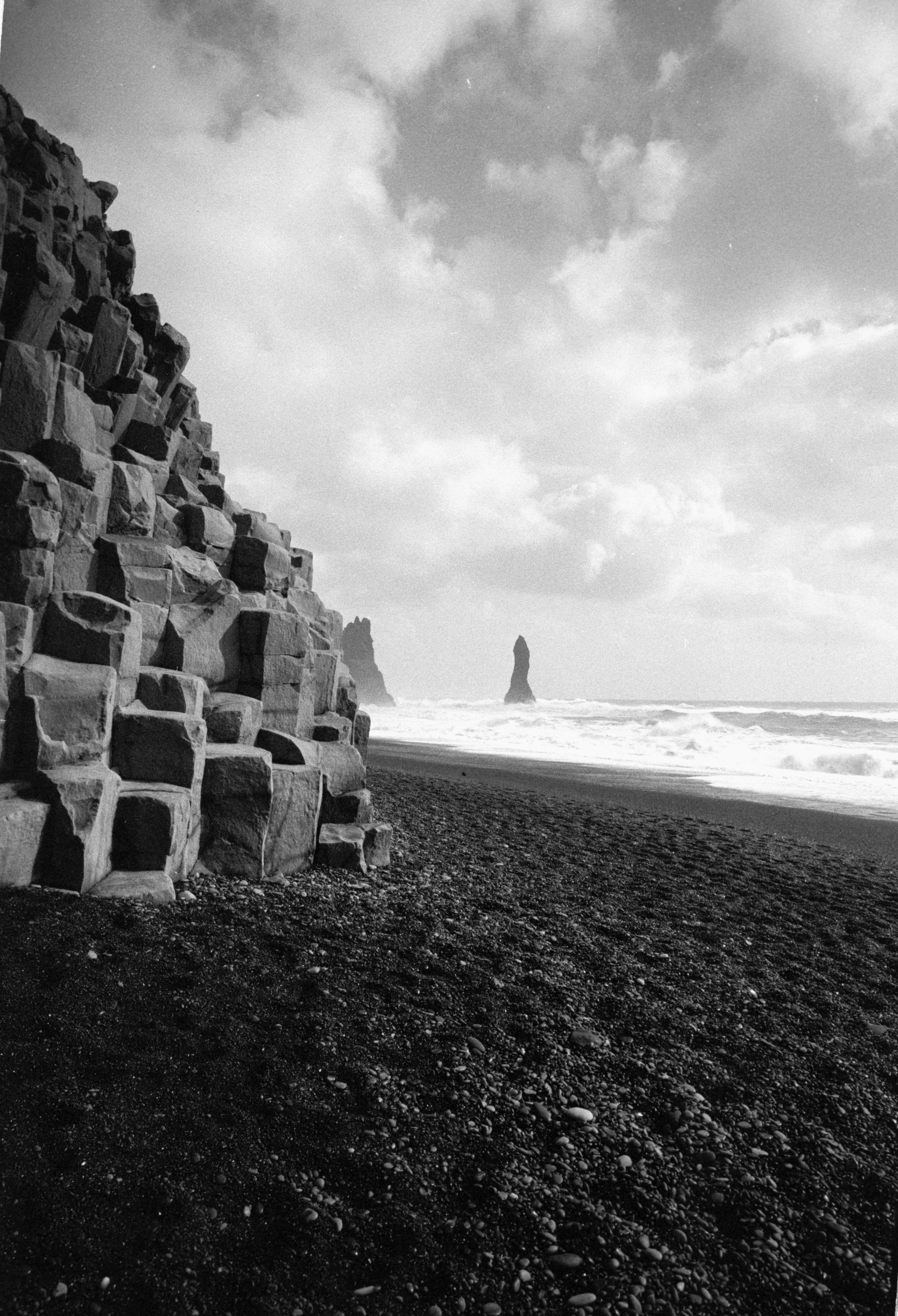 Basalt columns on a black sand beach with ocean waves.