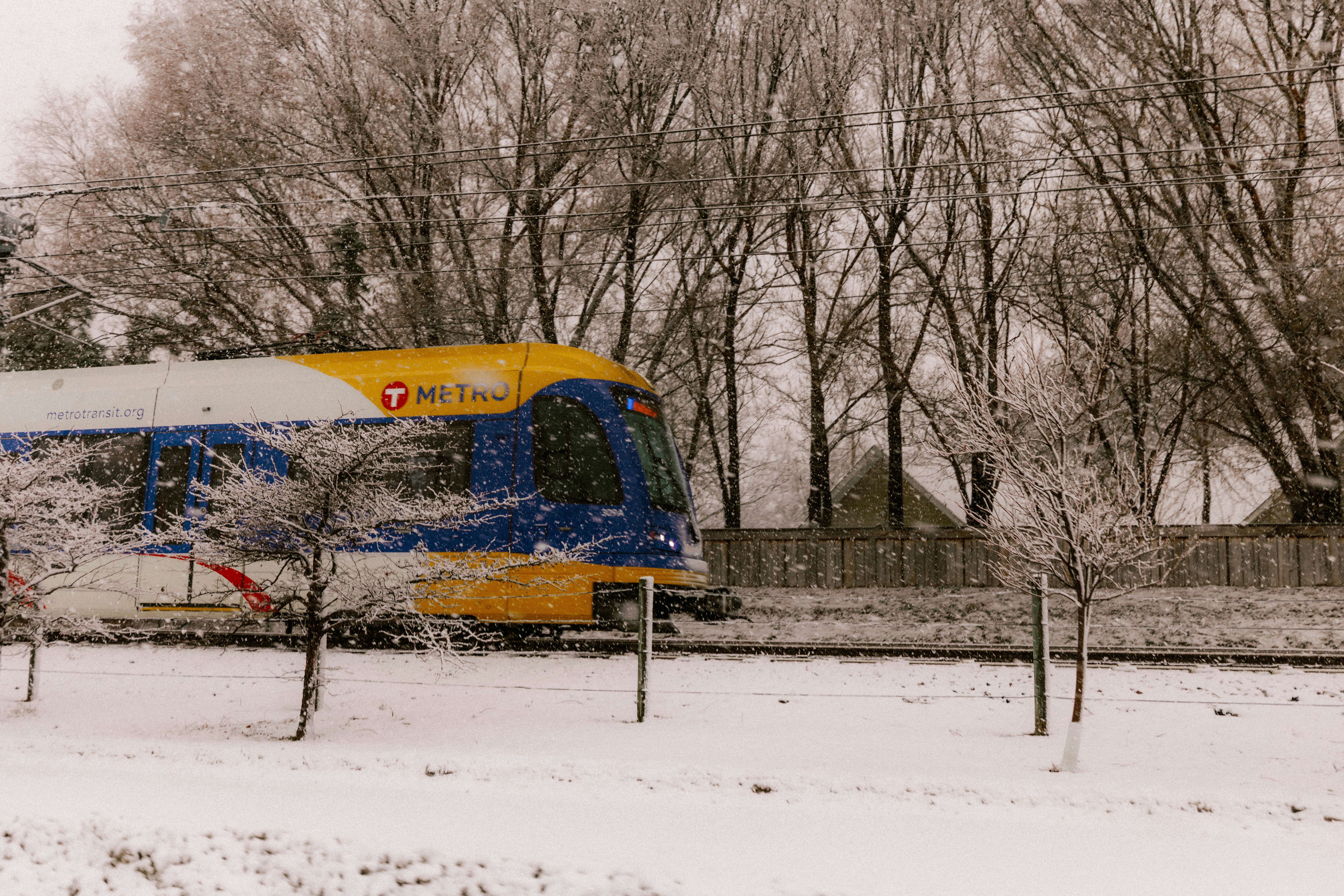 Yellow-Blue Metro Train Rushing Through Snowed-Backdrop