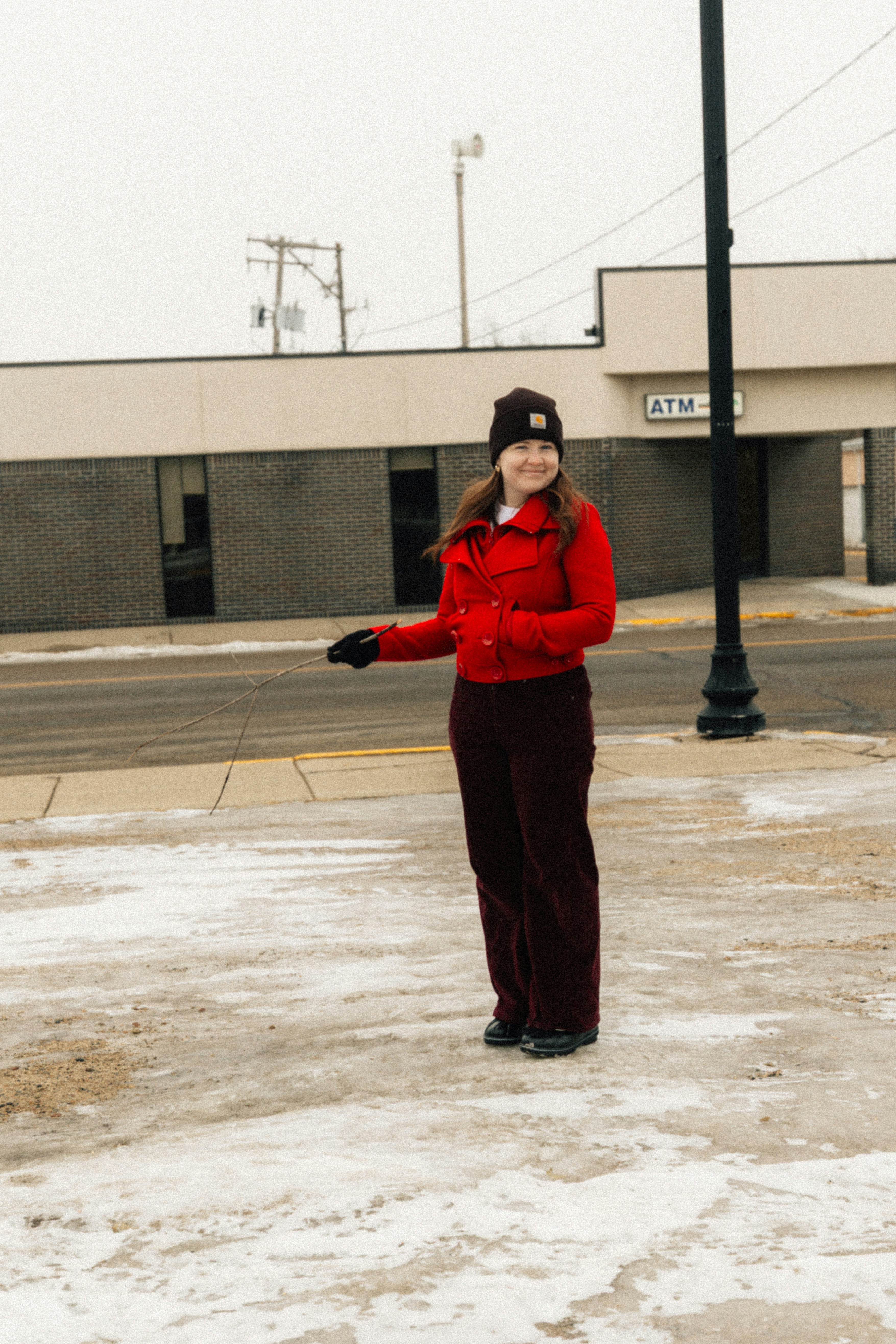 Red-coated figure in a snow-dusted lot by an ATM building