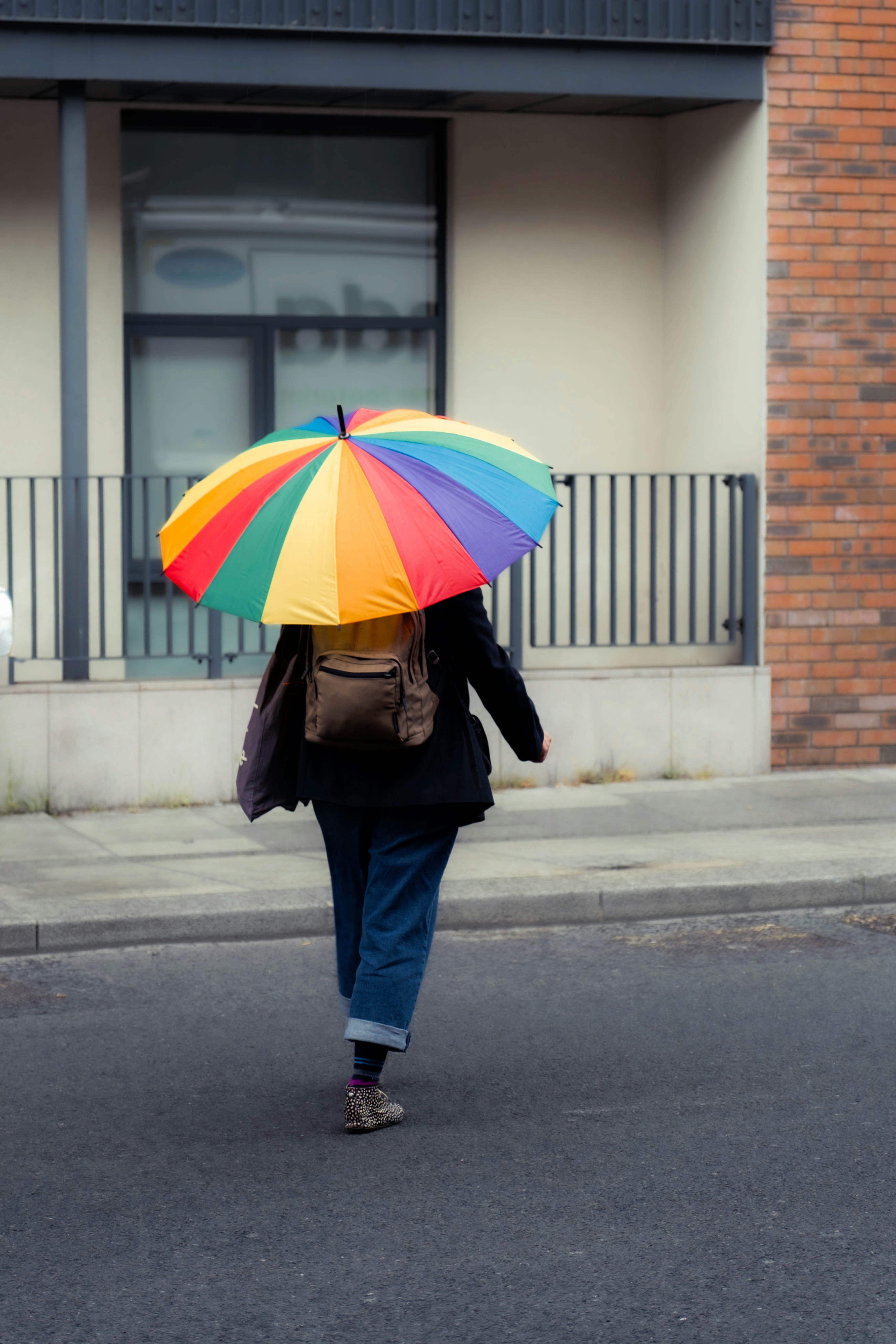 Chromatic Arc: A Pedestrian with a Rainbow Shelter Walks Past an Urban Façade