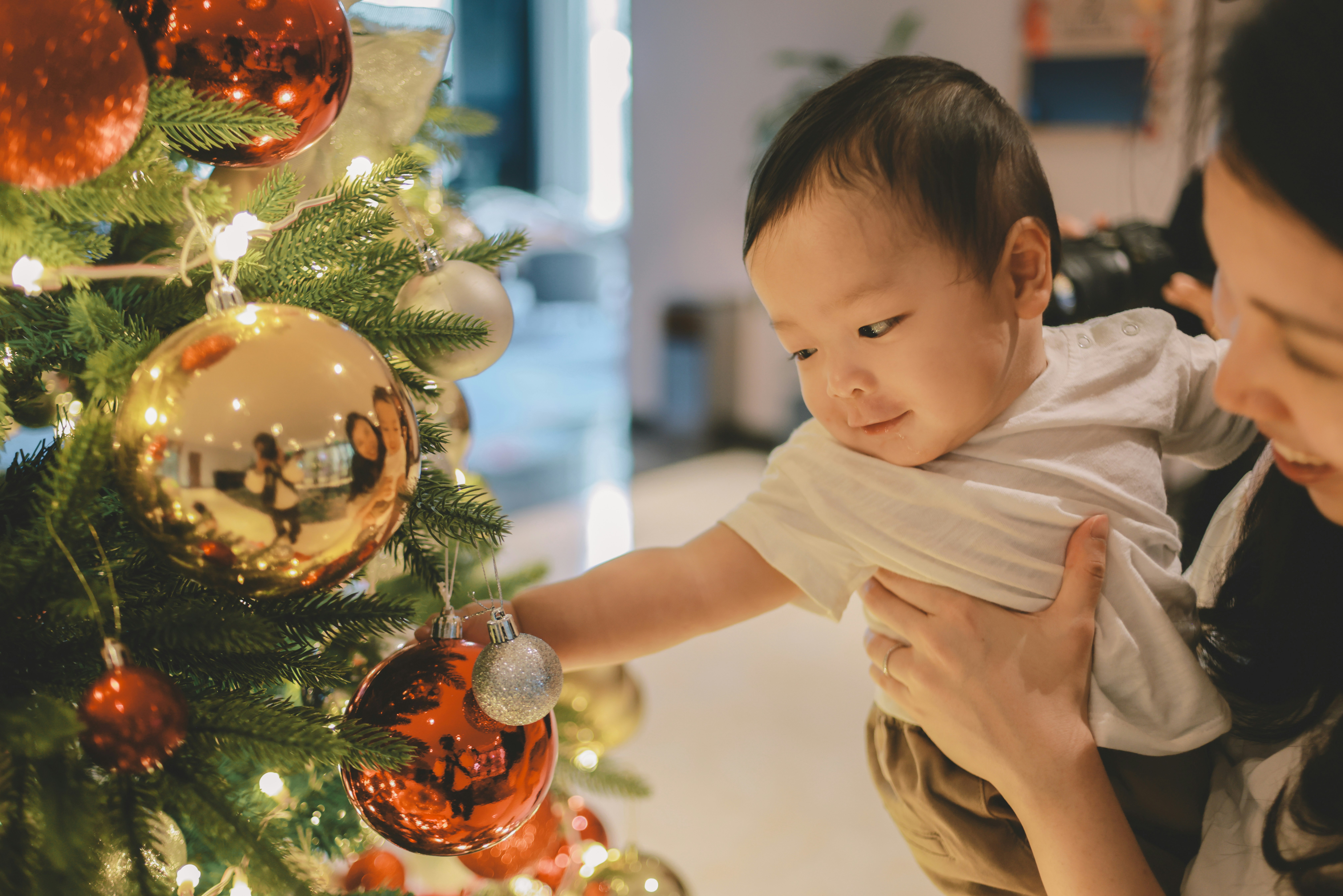 Gentle Christmas Moment: Baby Reach for the Tree Orbs as Parent Holds On