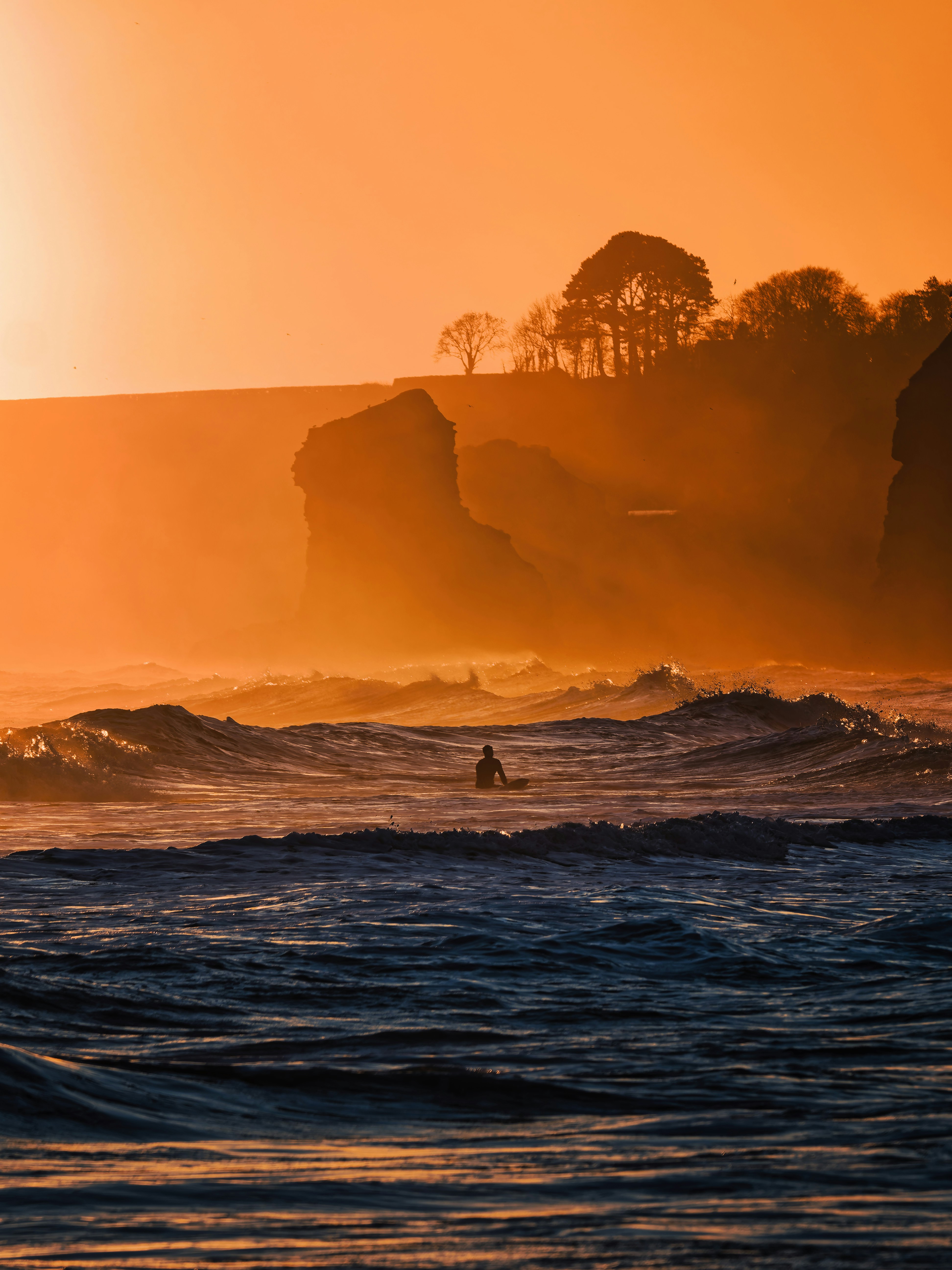 Waiting On the World to Change. A surfer biding his time at sunset on Christmas Eve along the Jurassic Coast, Devon, UK