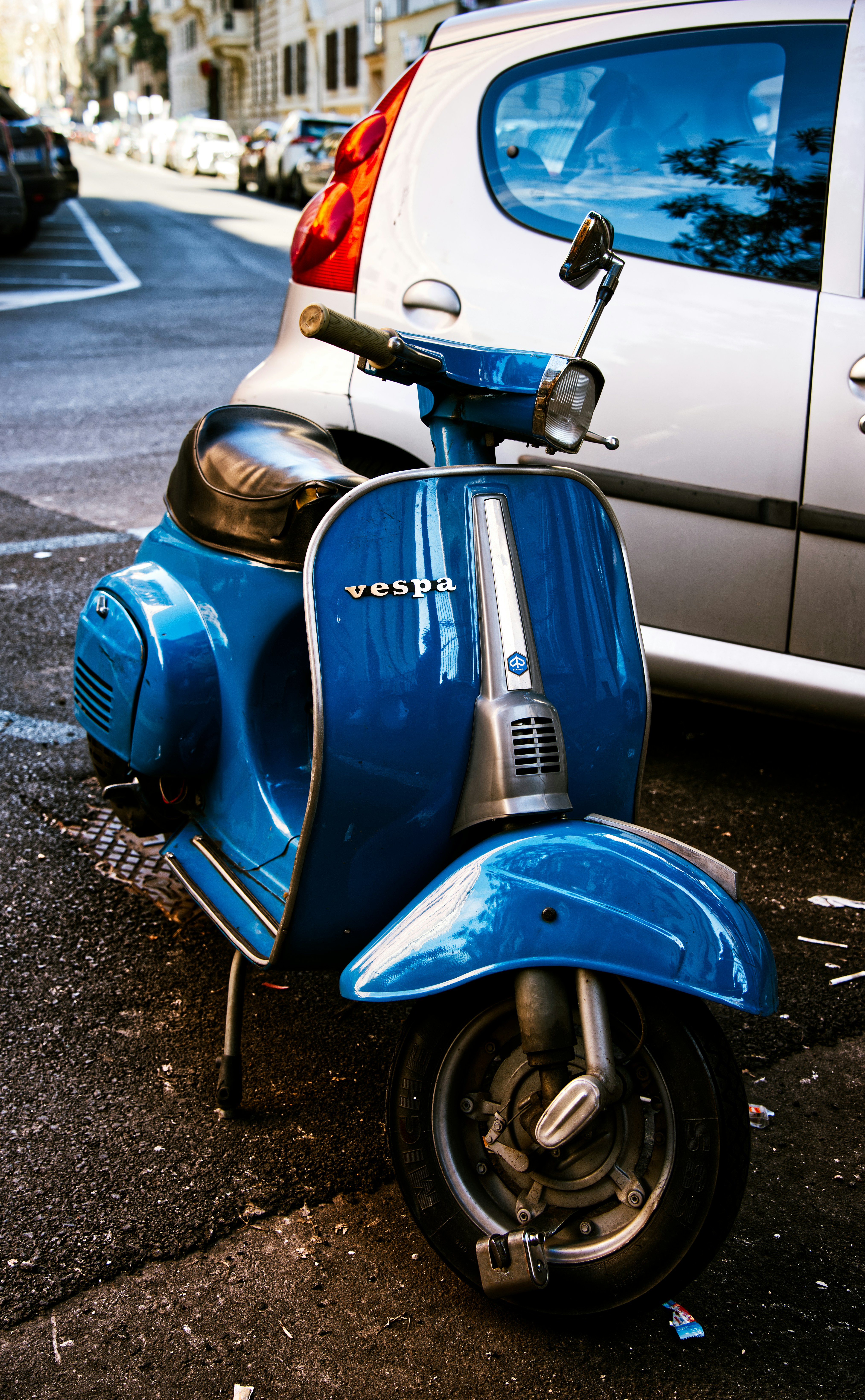 Navy Vespa Leaning Against a City Car