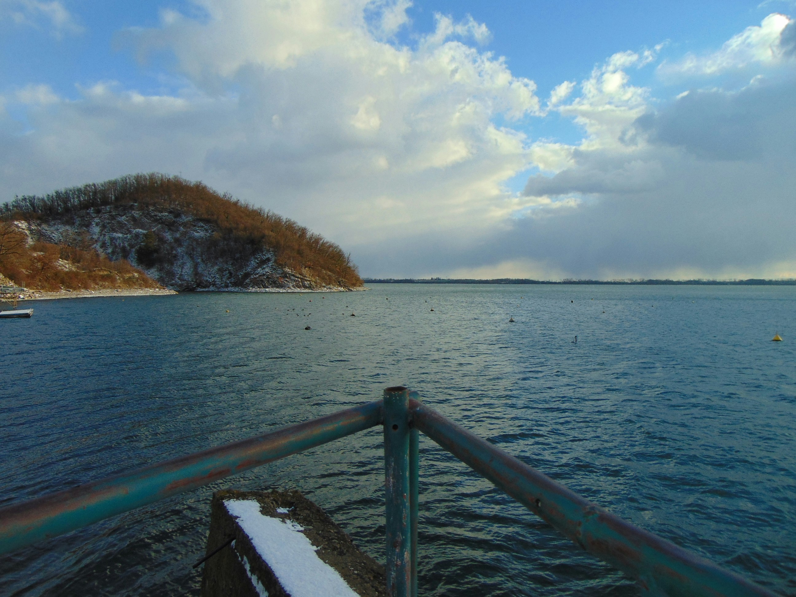 Rusted railing with snow-kissed promontory over a calm bay