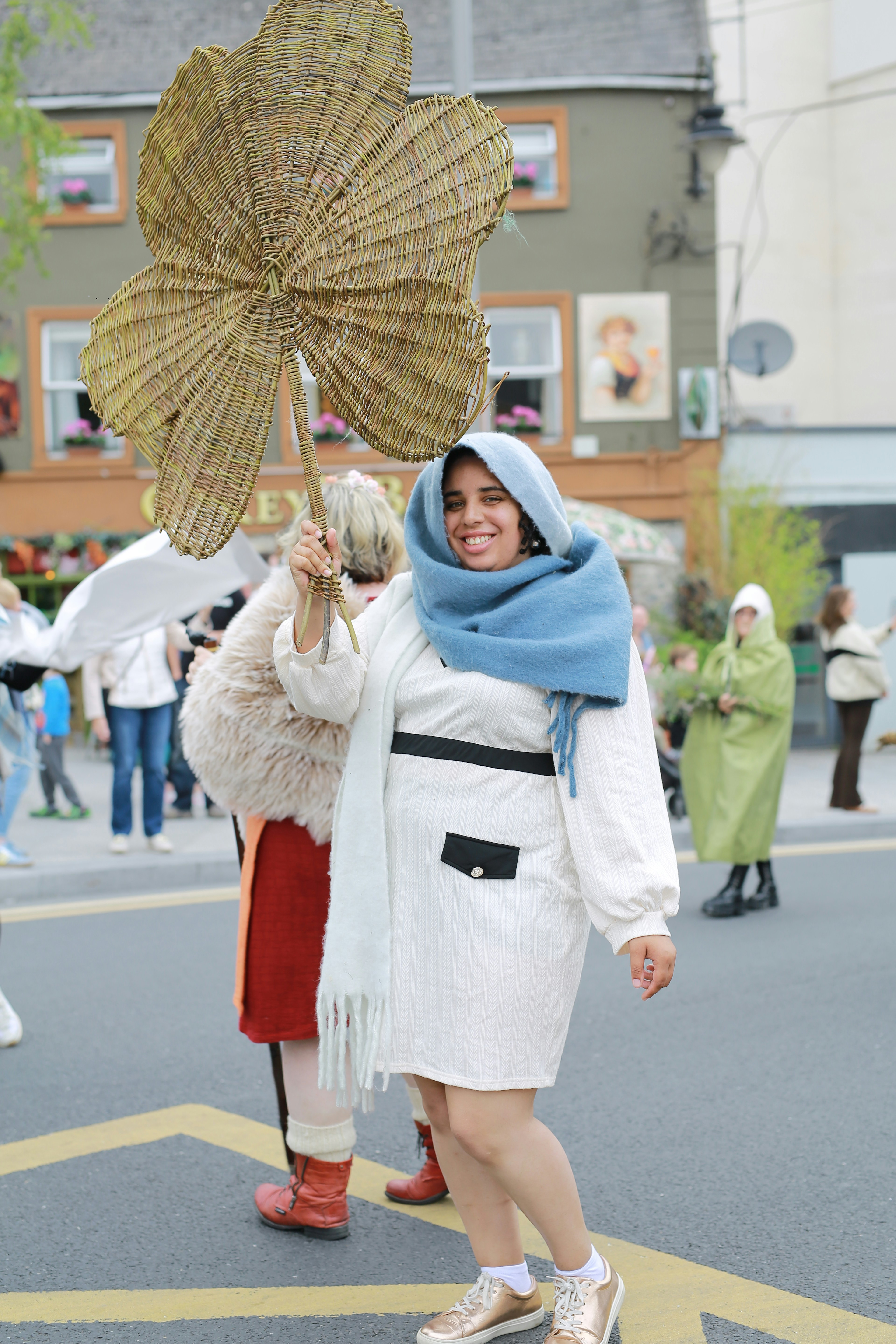 Joyful parade participant with oversized woven parasol on a sunny street