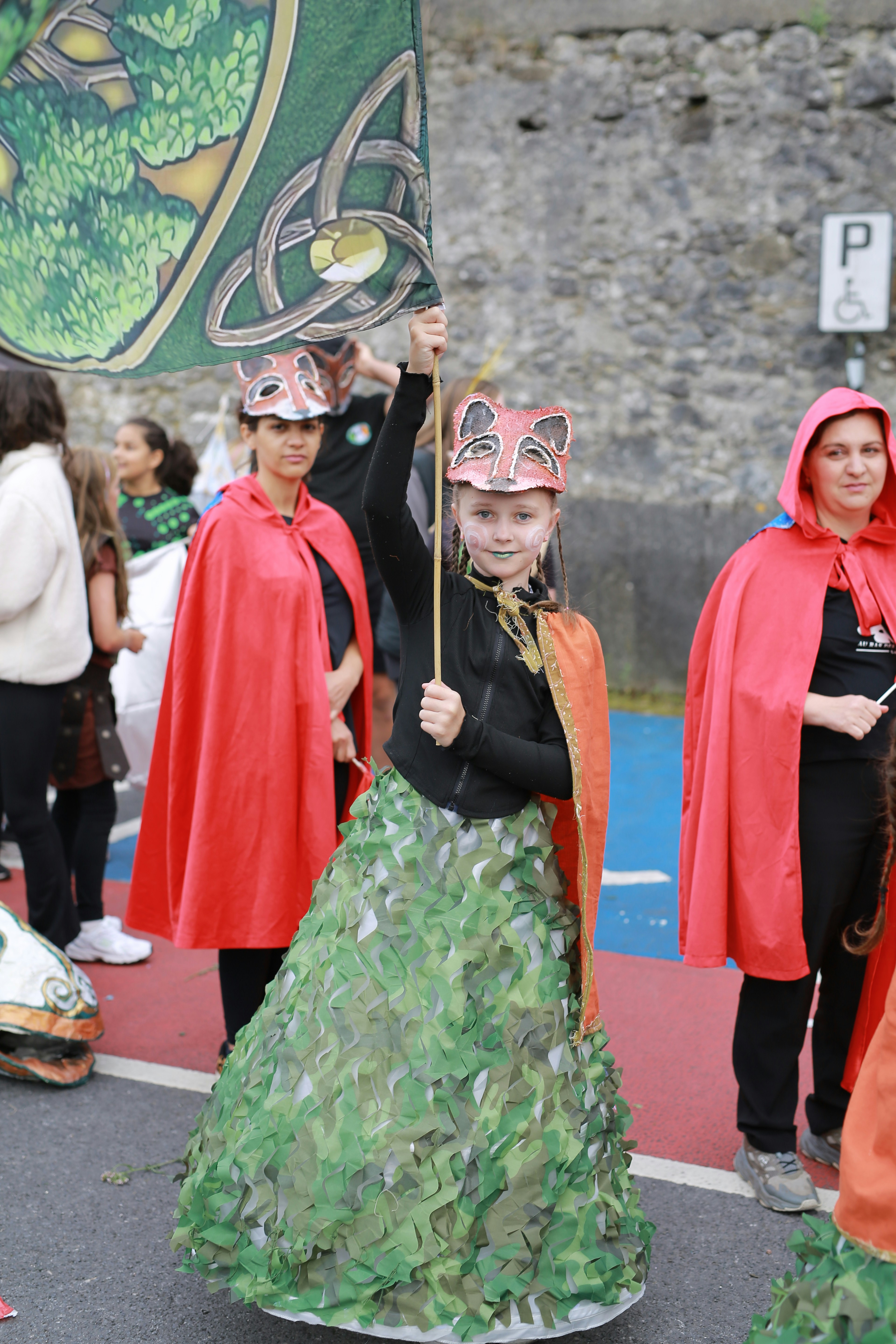 Masked Flag Bearer in a Green Leaf Gown at a Colorful Parade