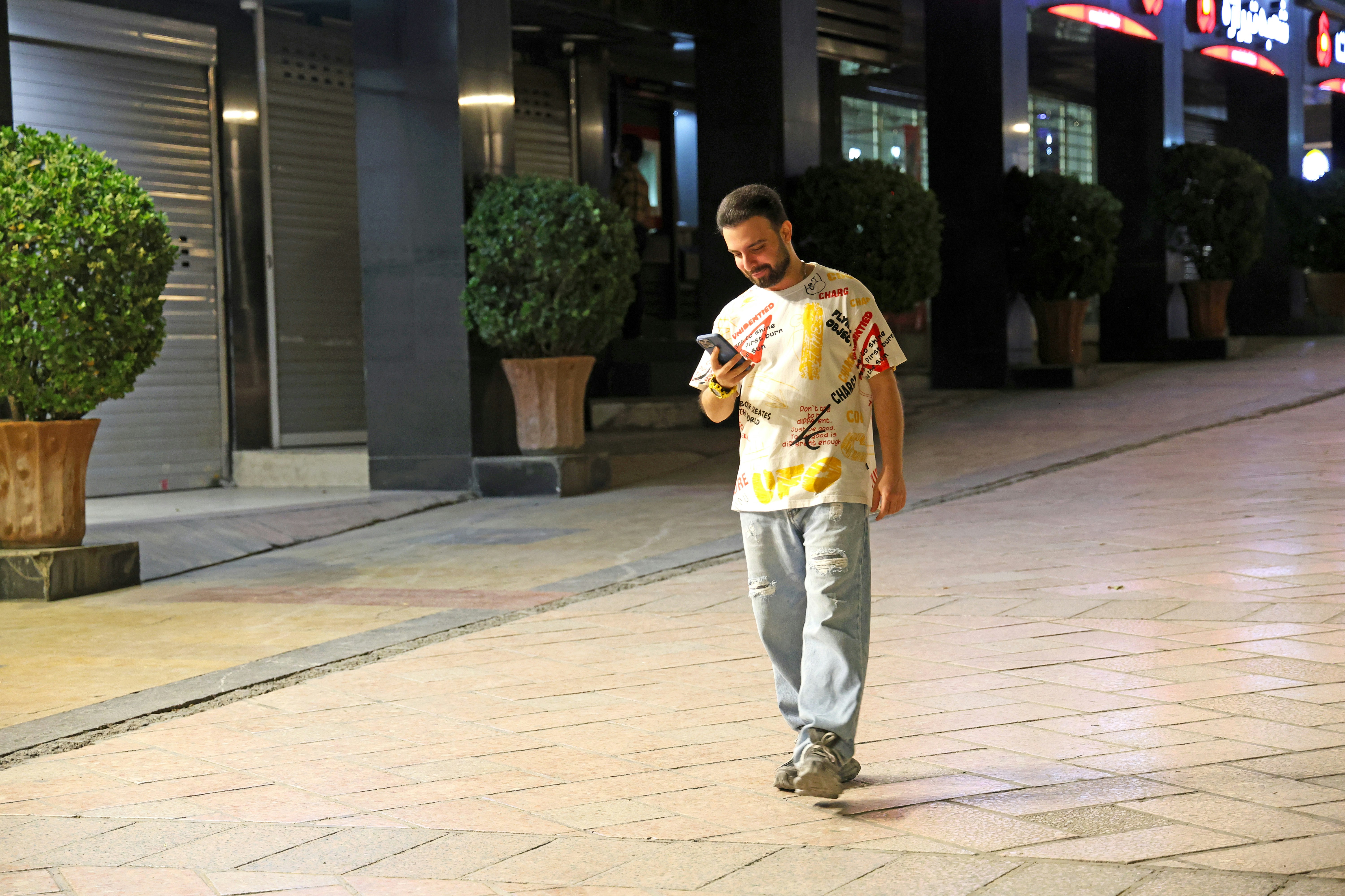 Lone pedestrian reads a page under streetlights in a quiet evening precinct