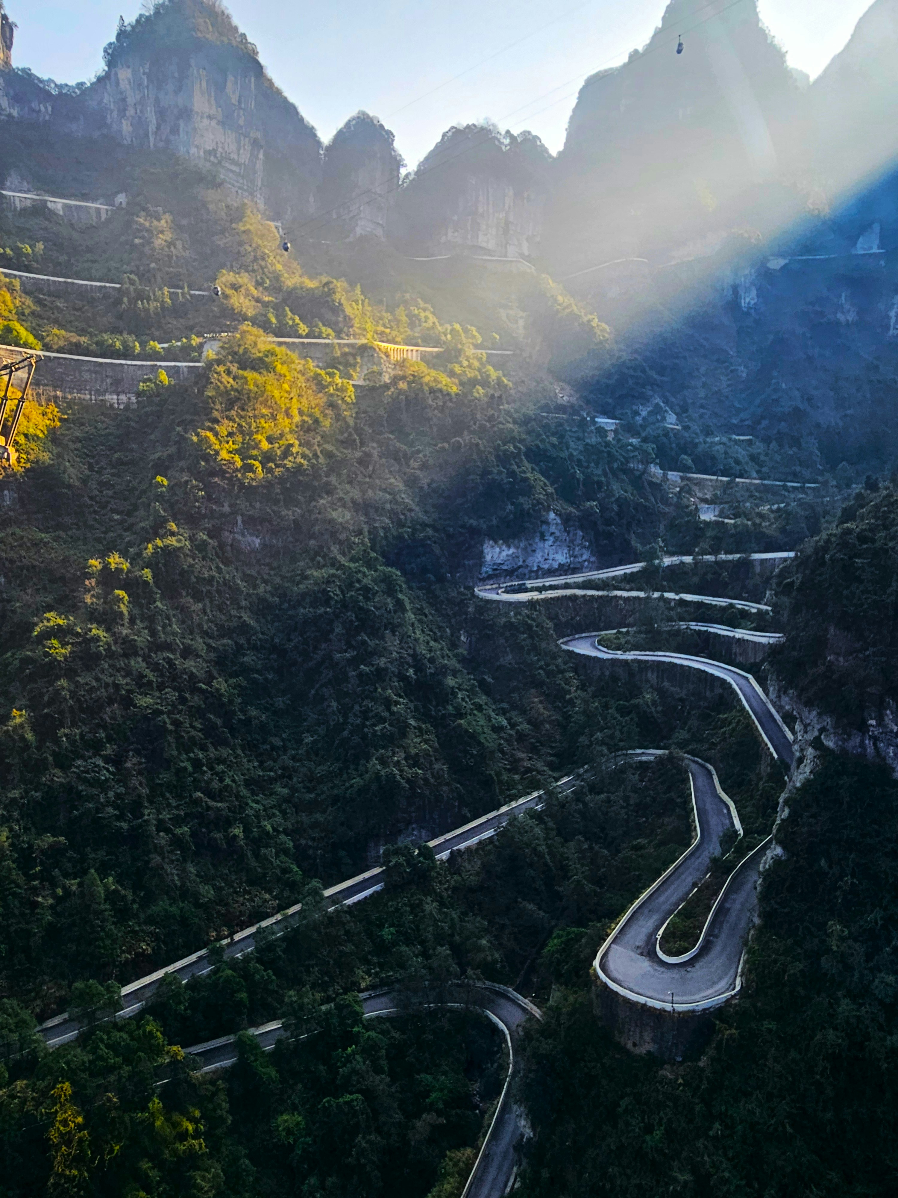 Winding mountain road with sunbeams through clouds.