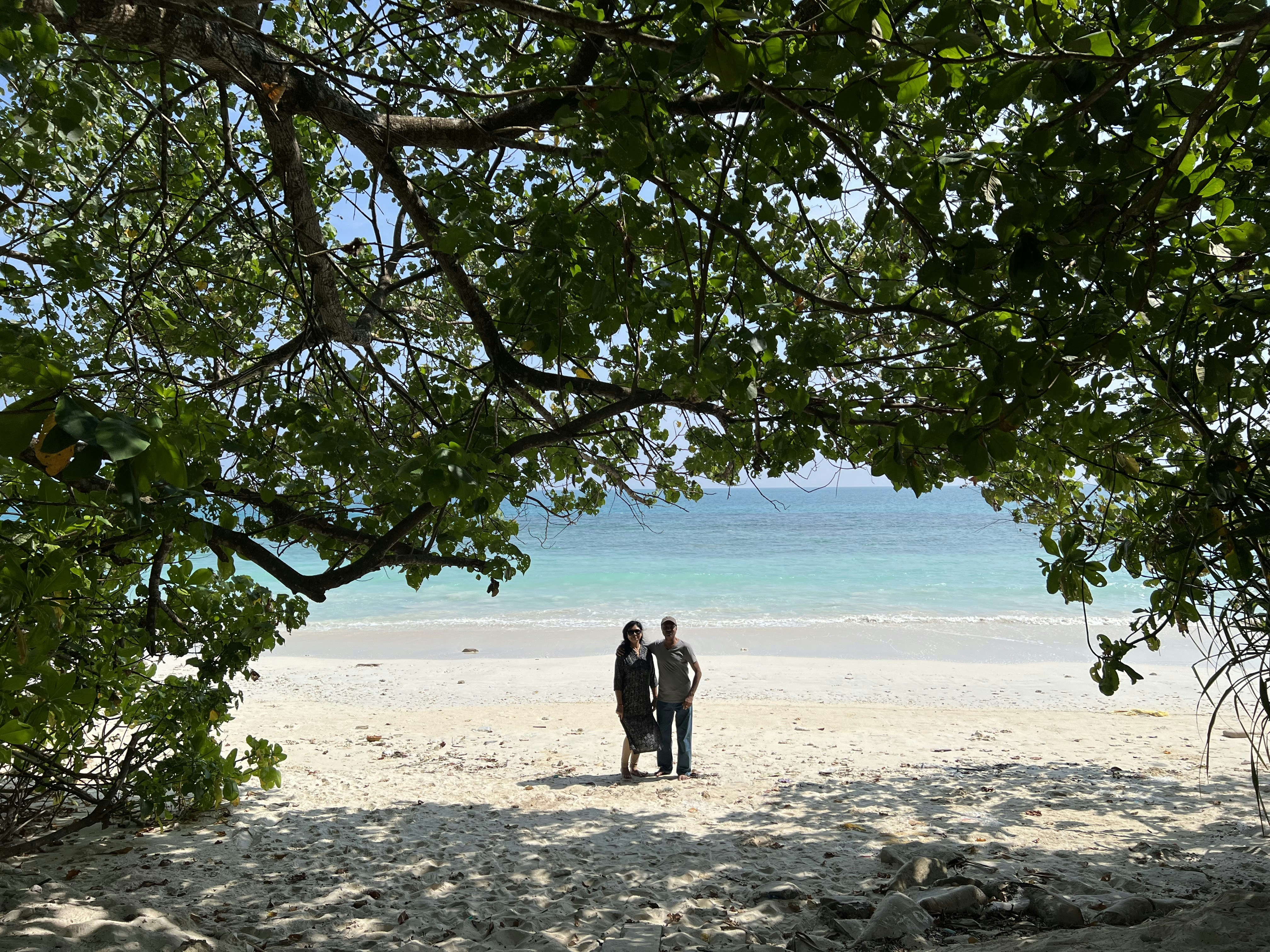 Couple on a sunlit tropical beach framed by leafy arches