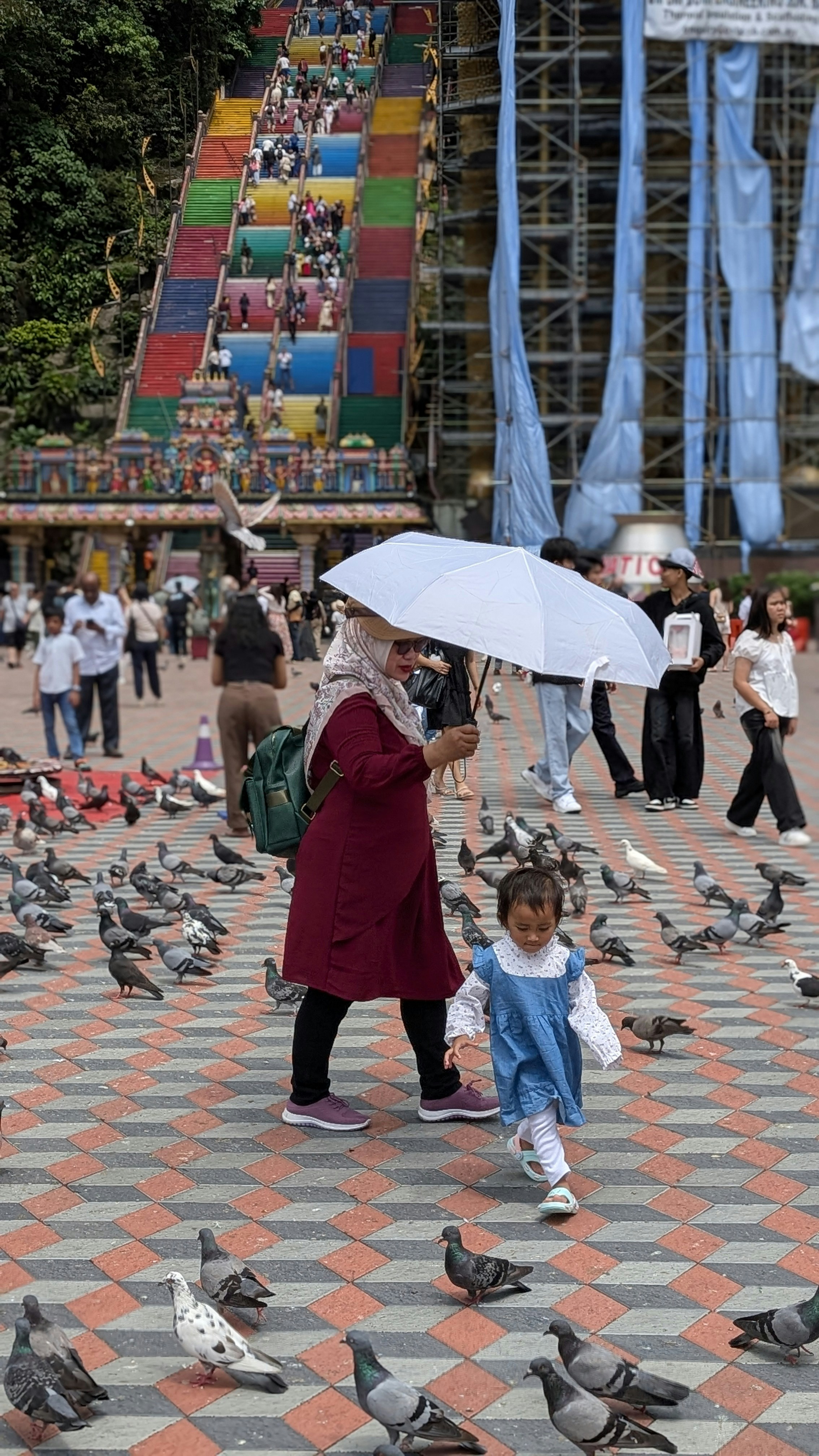 Woman with umbrella and child walk among pigeons.
