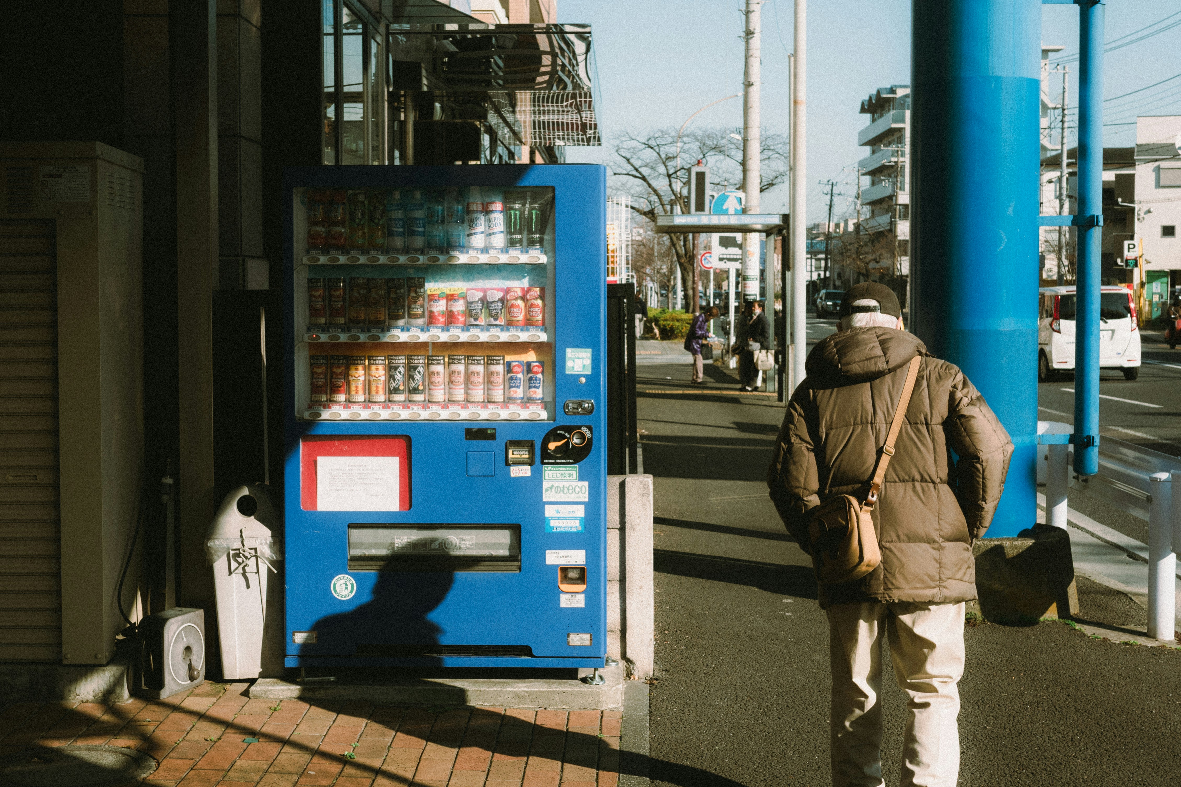 Blue Vending Machine, Shadowed Alley, and Striding Figure