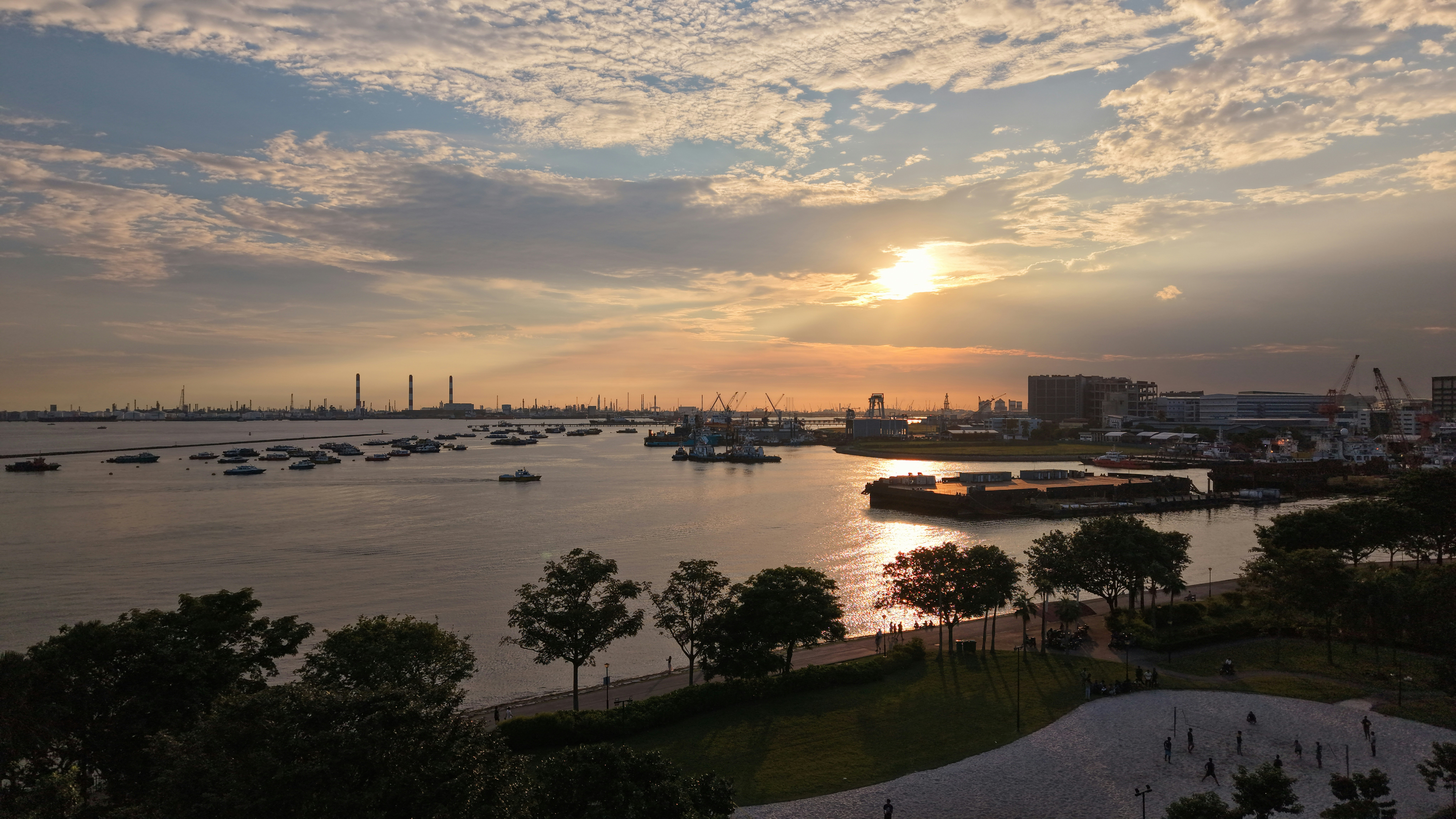 Sunset over a harbor with boats and cityscape.