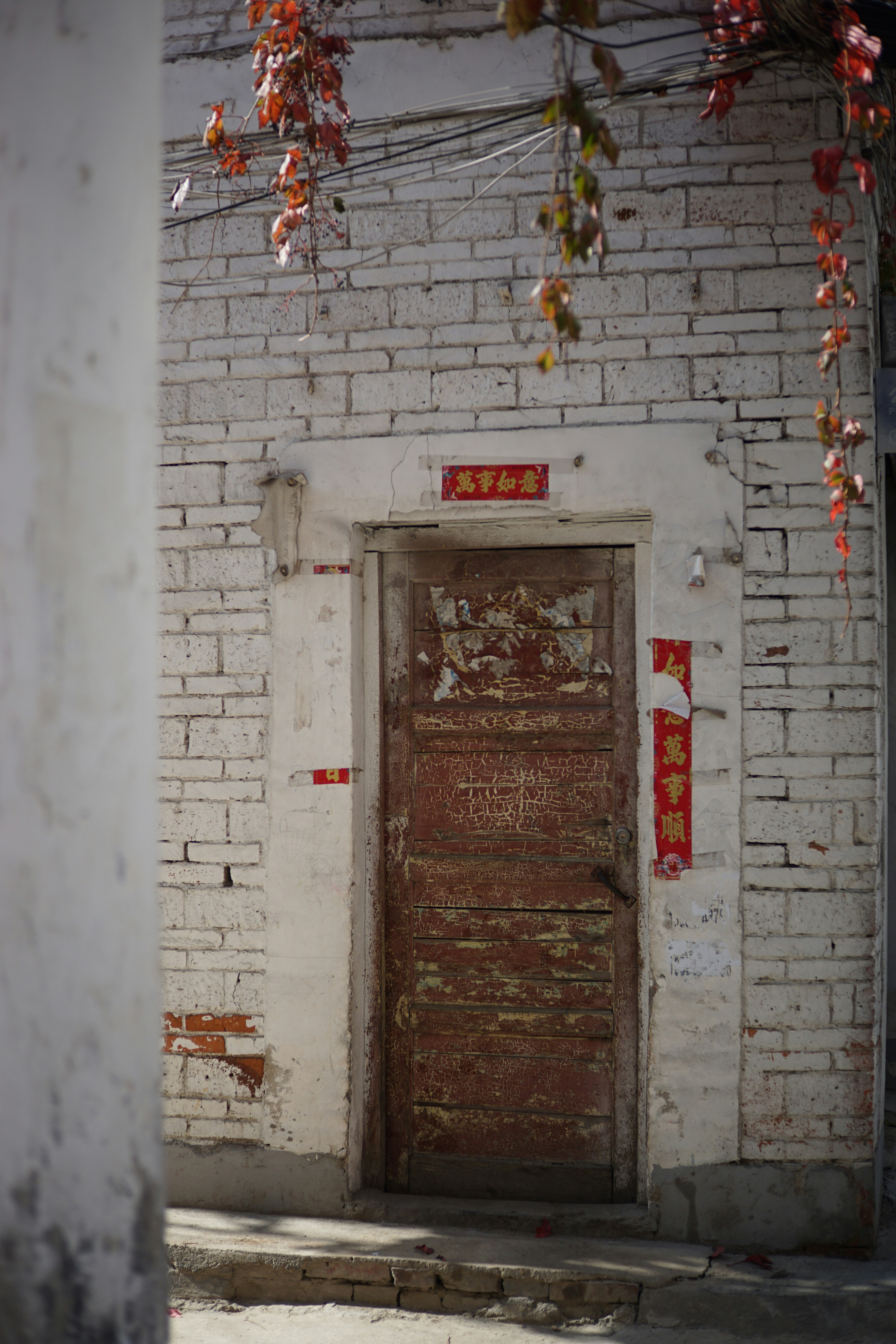 Weathered wooden door framed by white brick and red banners in a sunlit courtyard
