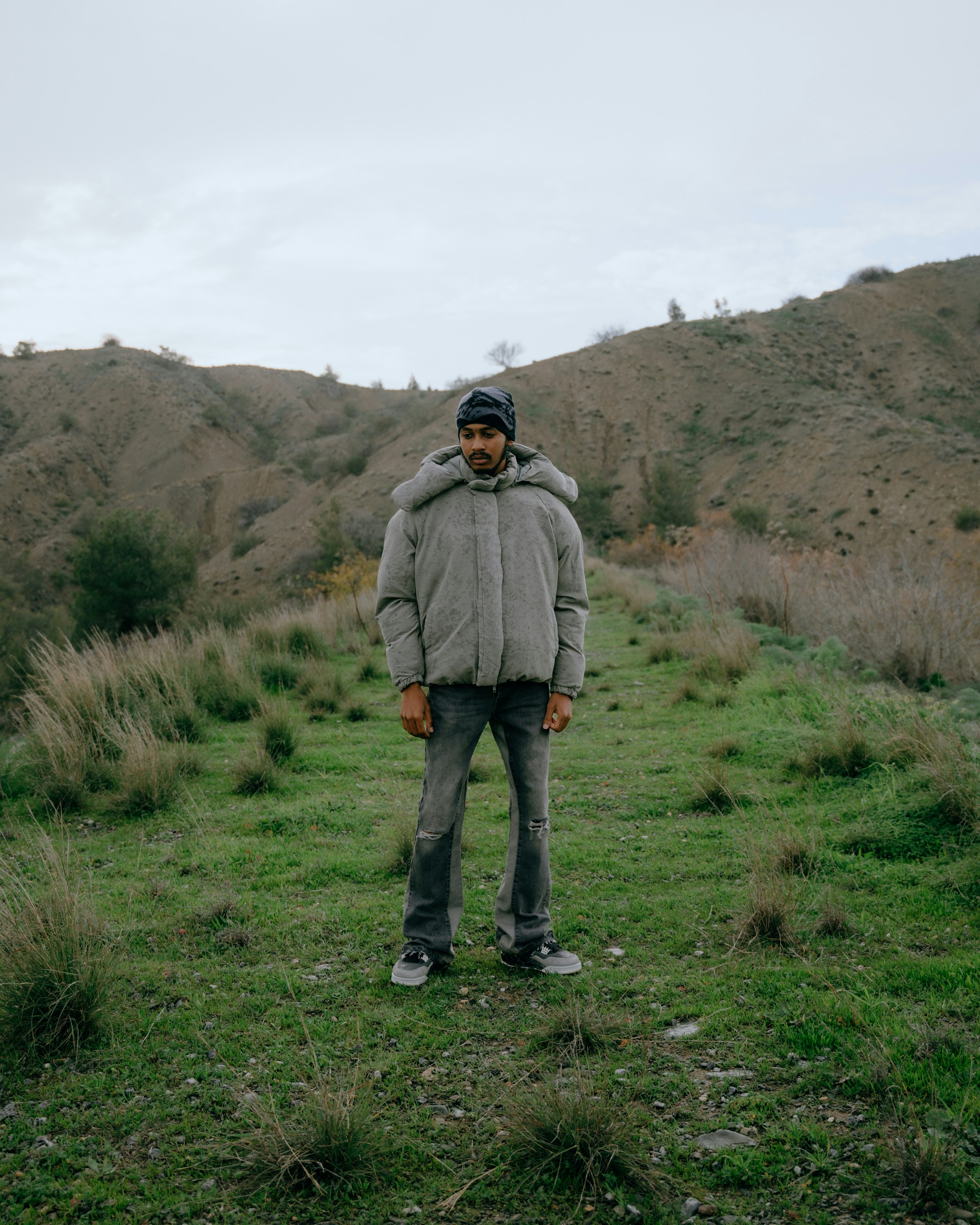 Lost among the hills: a lone figure in a puffy gray coat amid autumn grass