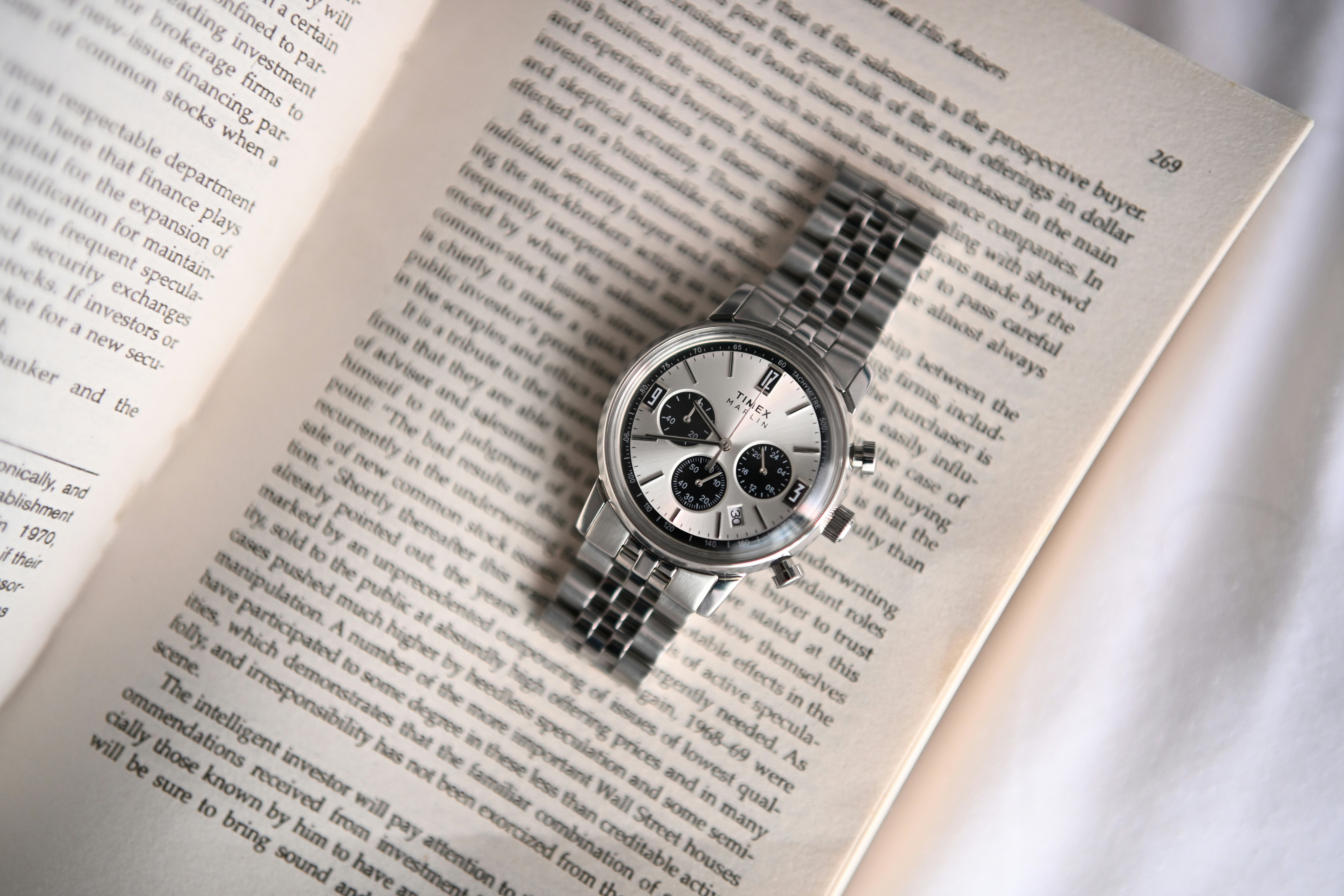 A silver watch rests on an open book.