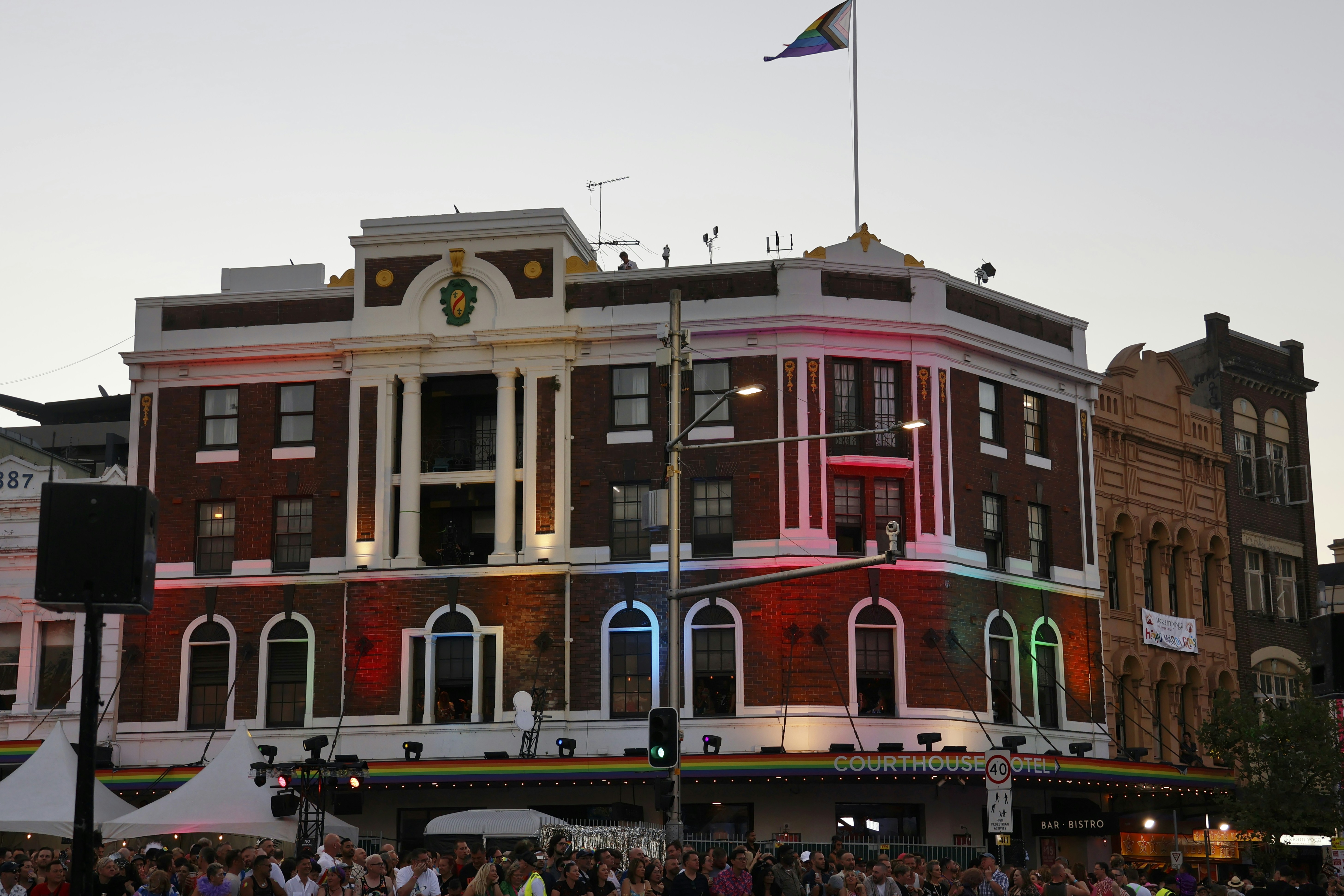 Historic pub facade lit with rainbow accents amid a crowded evening street scene