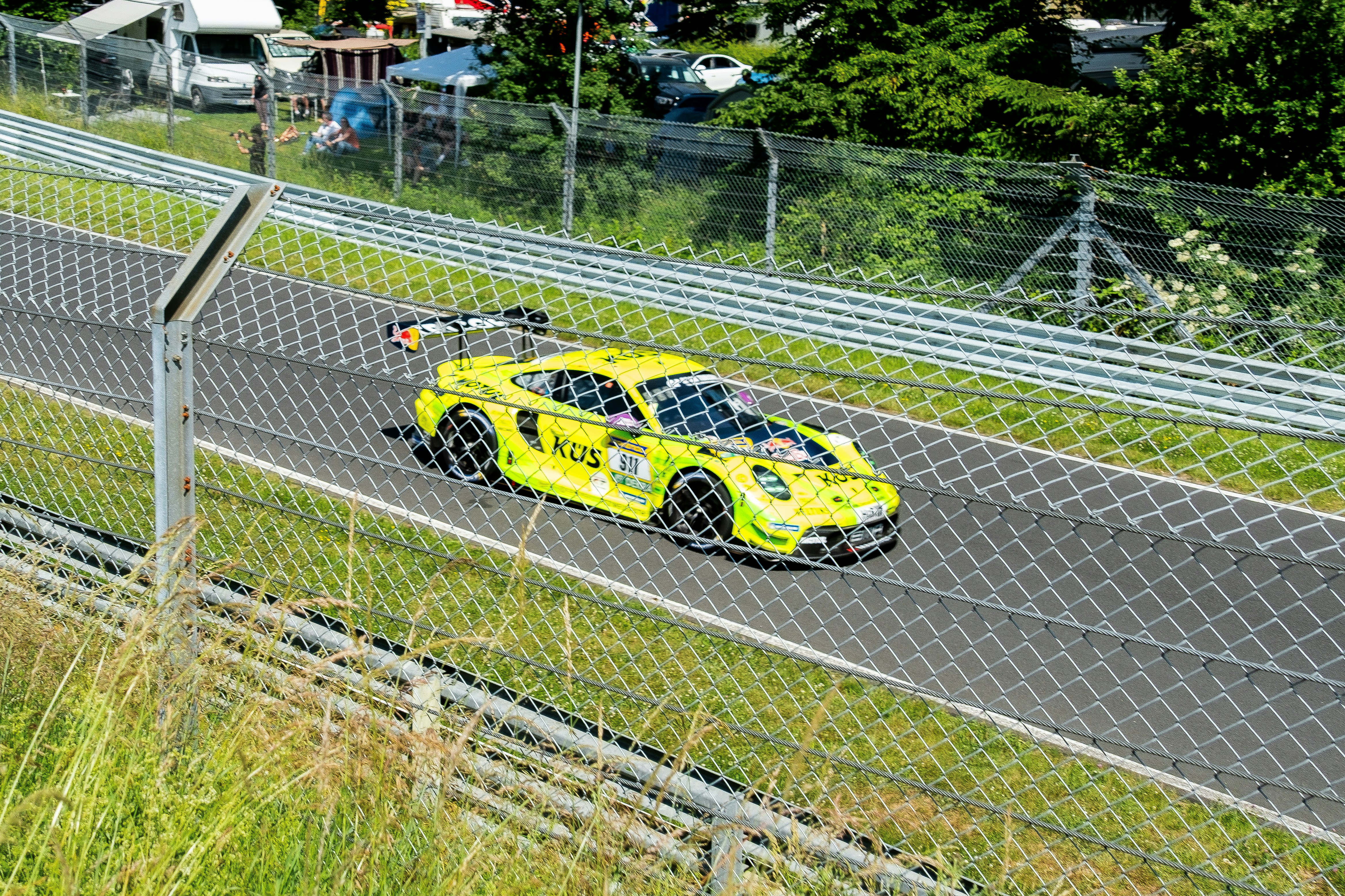Yellow race car slicing through the chicane under a chain-link fence
