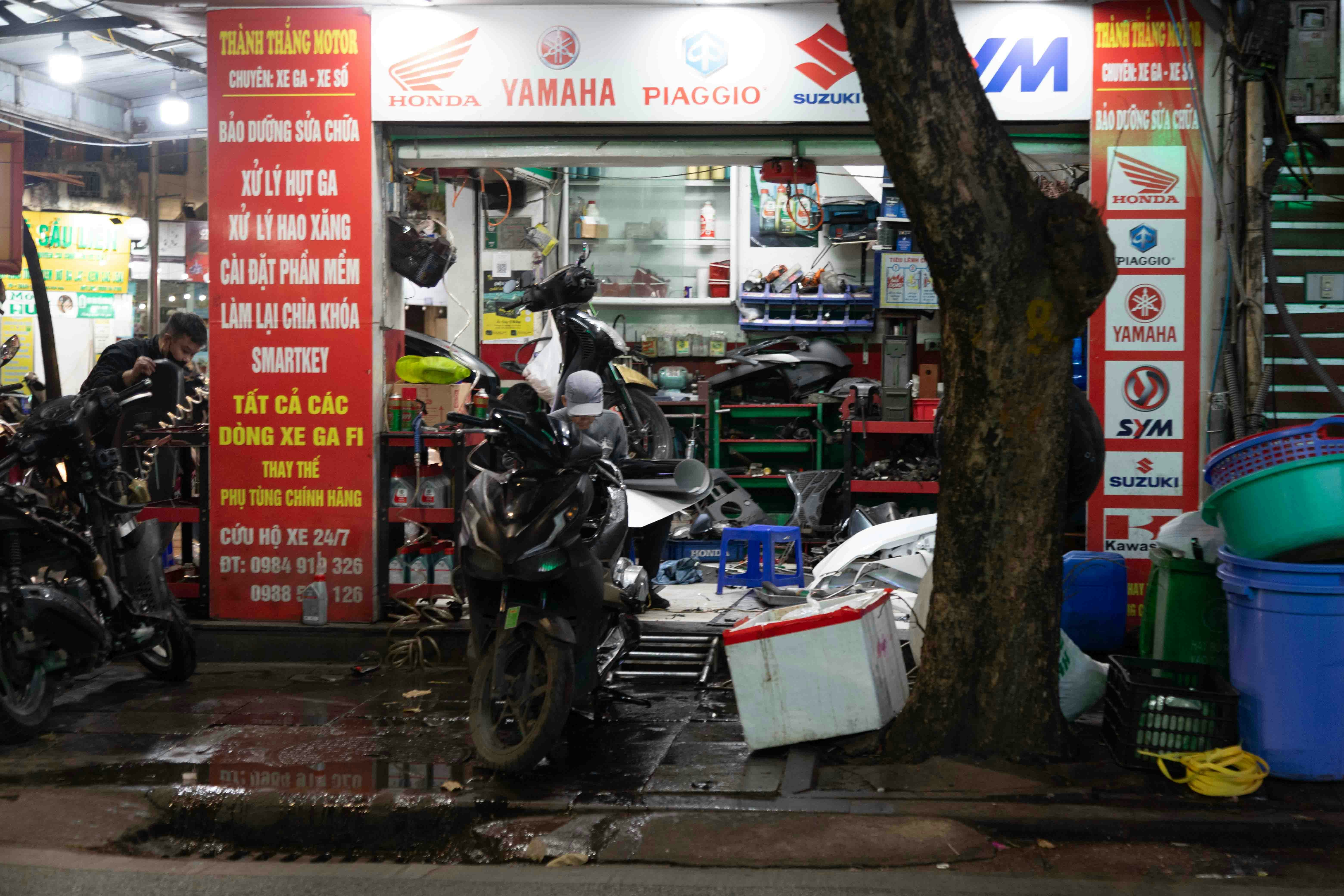 Rain-Slicked Streetfront Workshop Beneath Neon Advertisements
