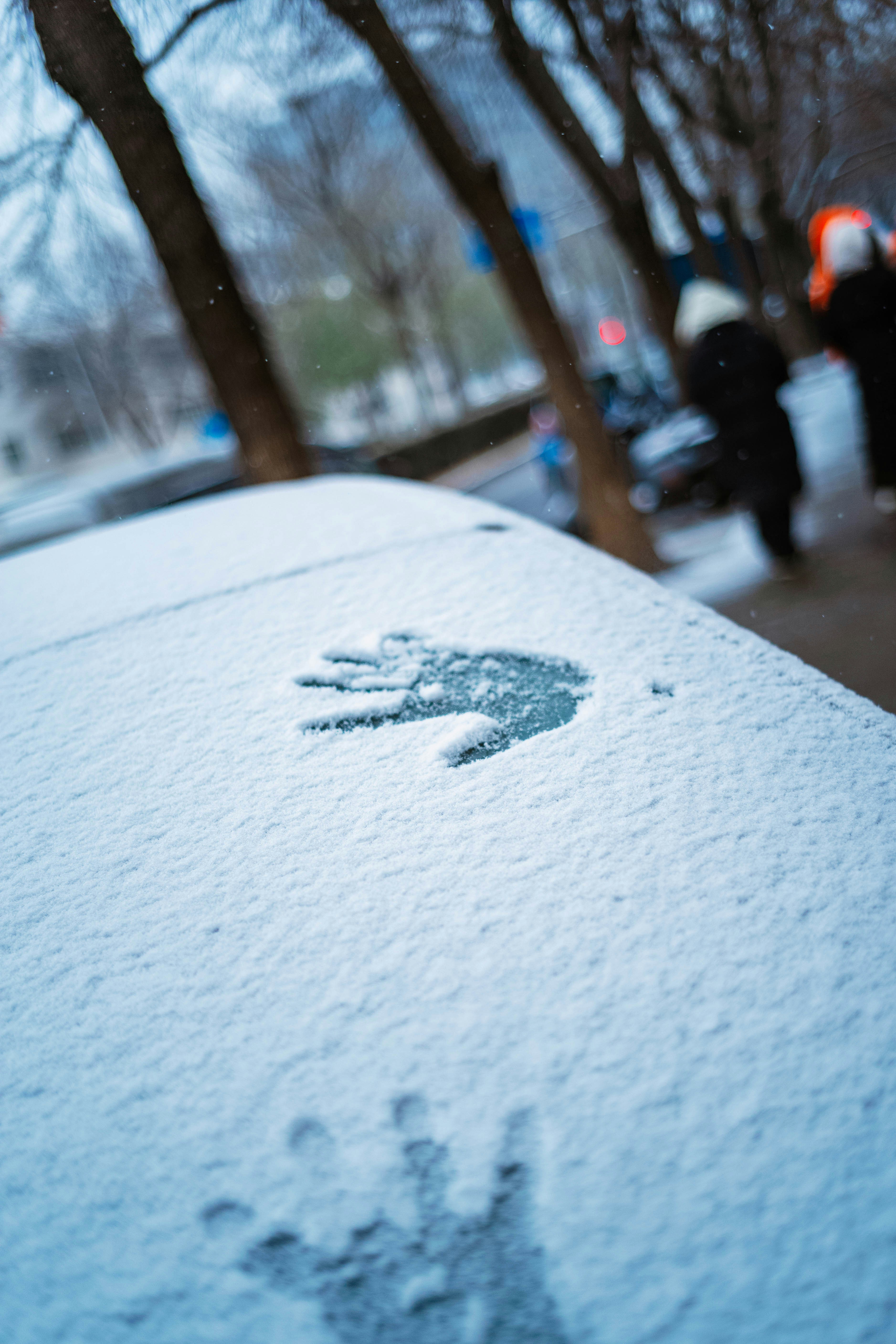 Snowy Handprint on a Frosted Car Surface with City Figures in the Background