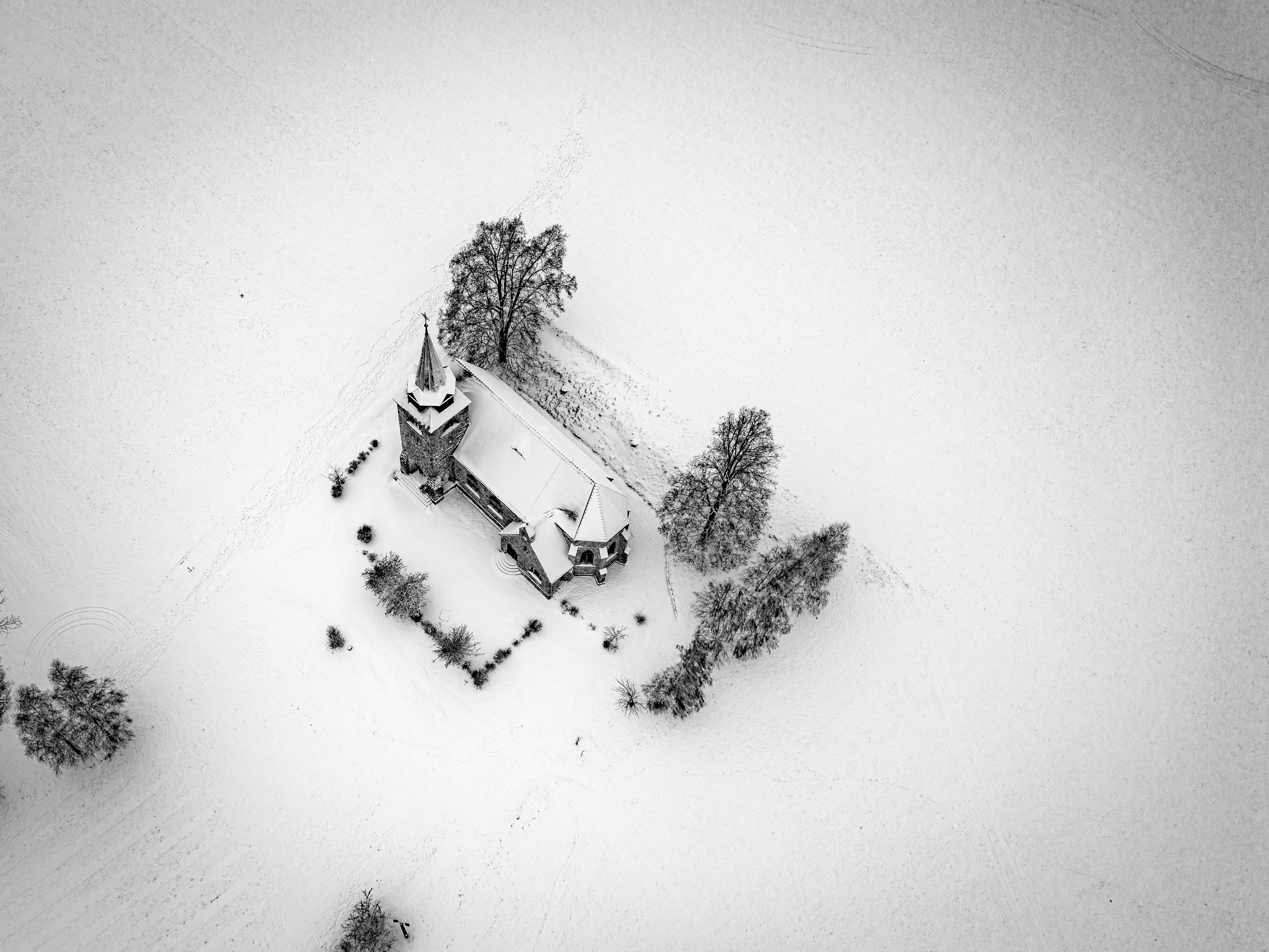 Minimalist aerial view of a small church in Borovnička surrounded by snow-covered fields. The black and white composition emphasizes isolation, silence, and the calm geometry of winter landscape.