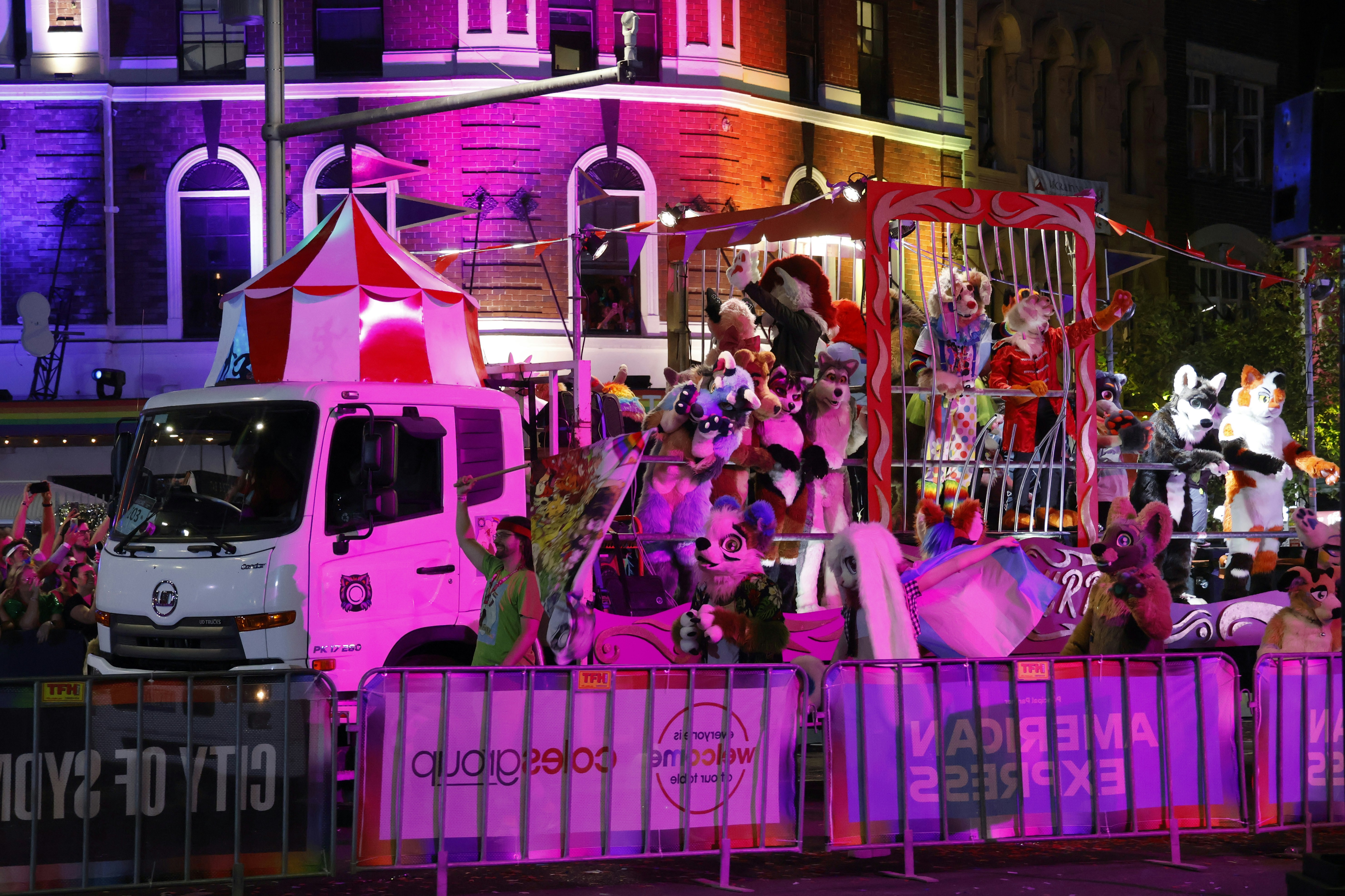 Vibrant parade float procession with costumed characters and a lit backdrop, captured at night; a festive, stage-like scene with colorful lighting and a vehicle as platform.
