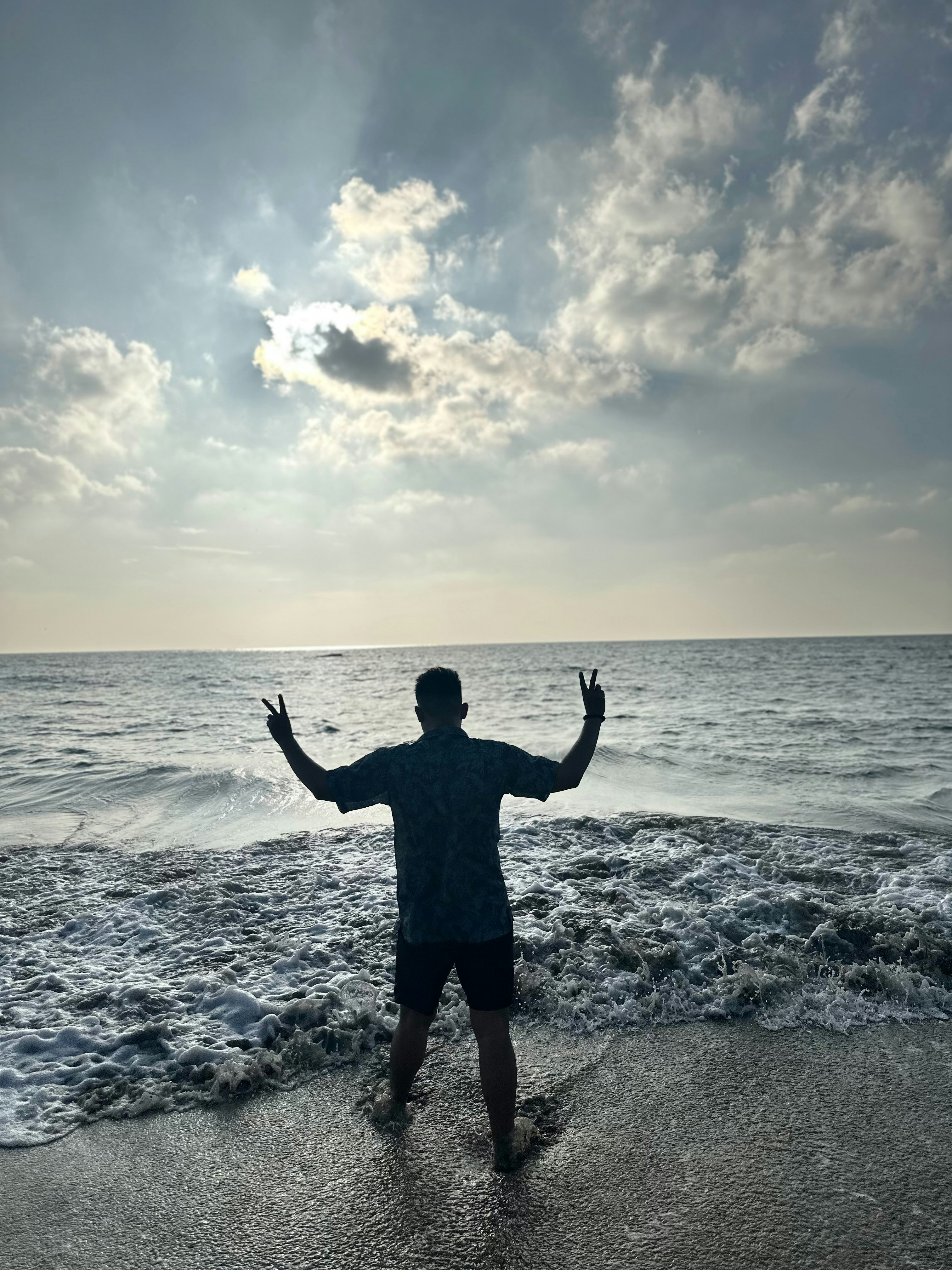 Silhouette at the Horizon: Man by the Sea with Raised Hands