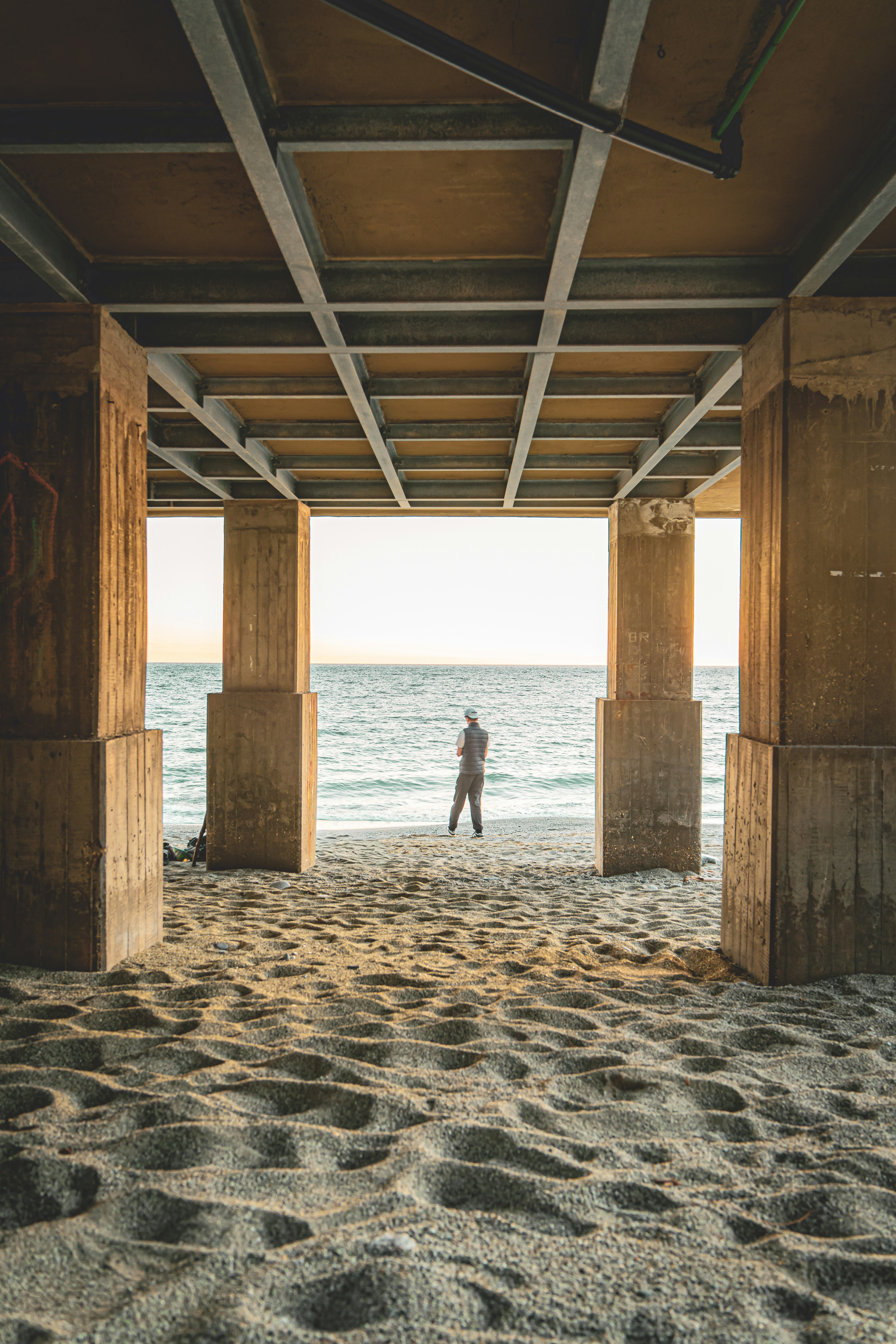 Lone figure beneath a concrete pier at the shoreline