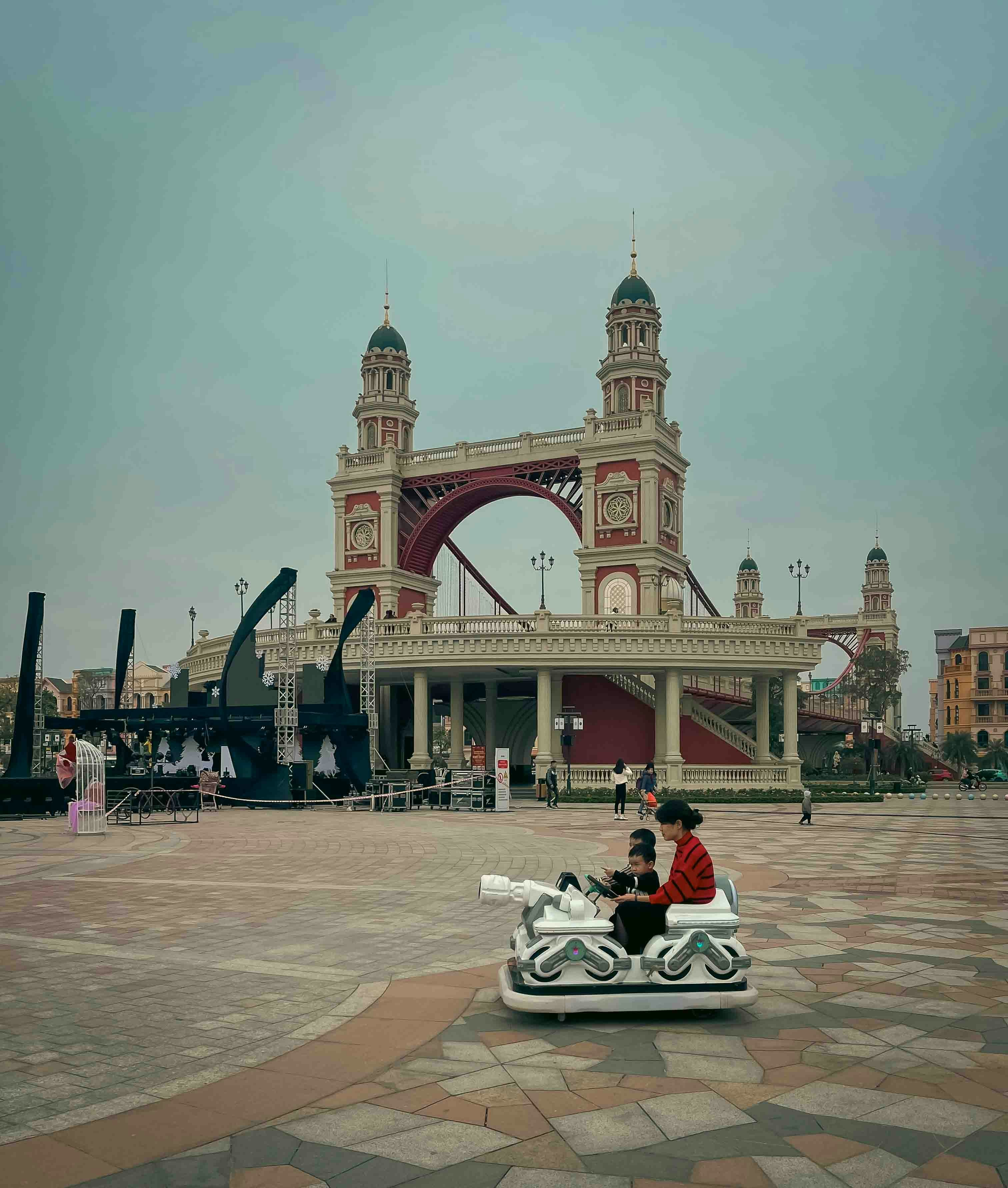 Cartoonish white ride turns under a grand arcade near a colonial arch at the waterfront
