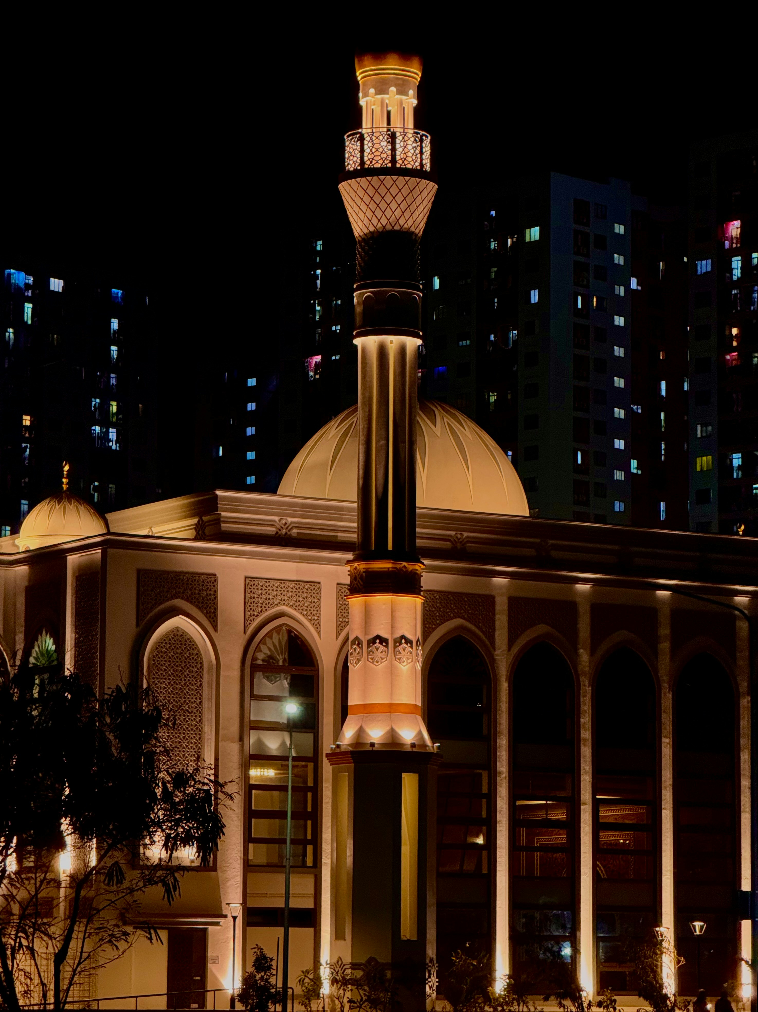 Illuminated minaret rises above a grand, arched facade at night