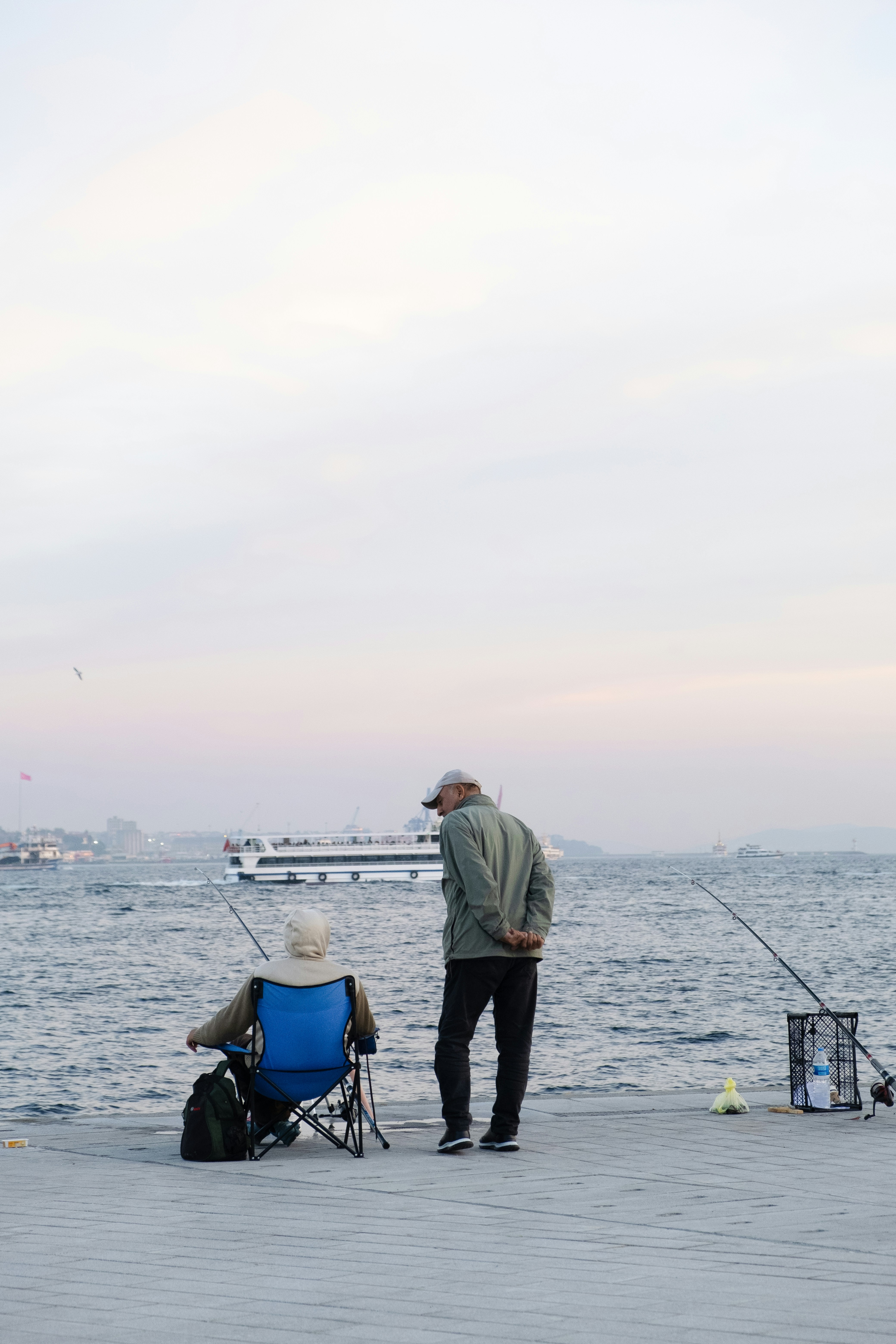 Quiet Pier Watch: A Seated Angler and a Standing Companion by the Water