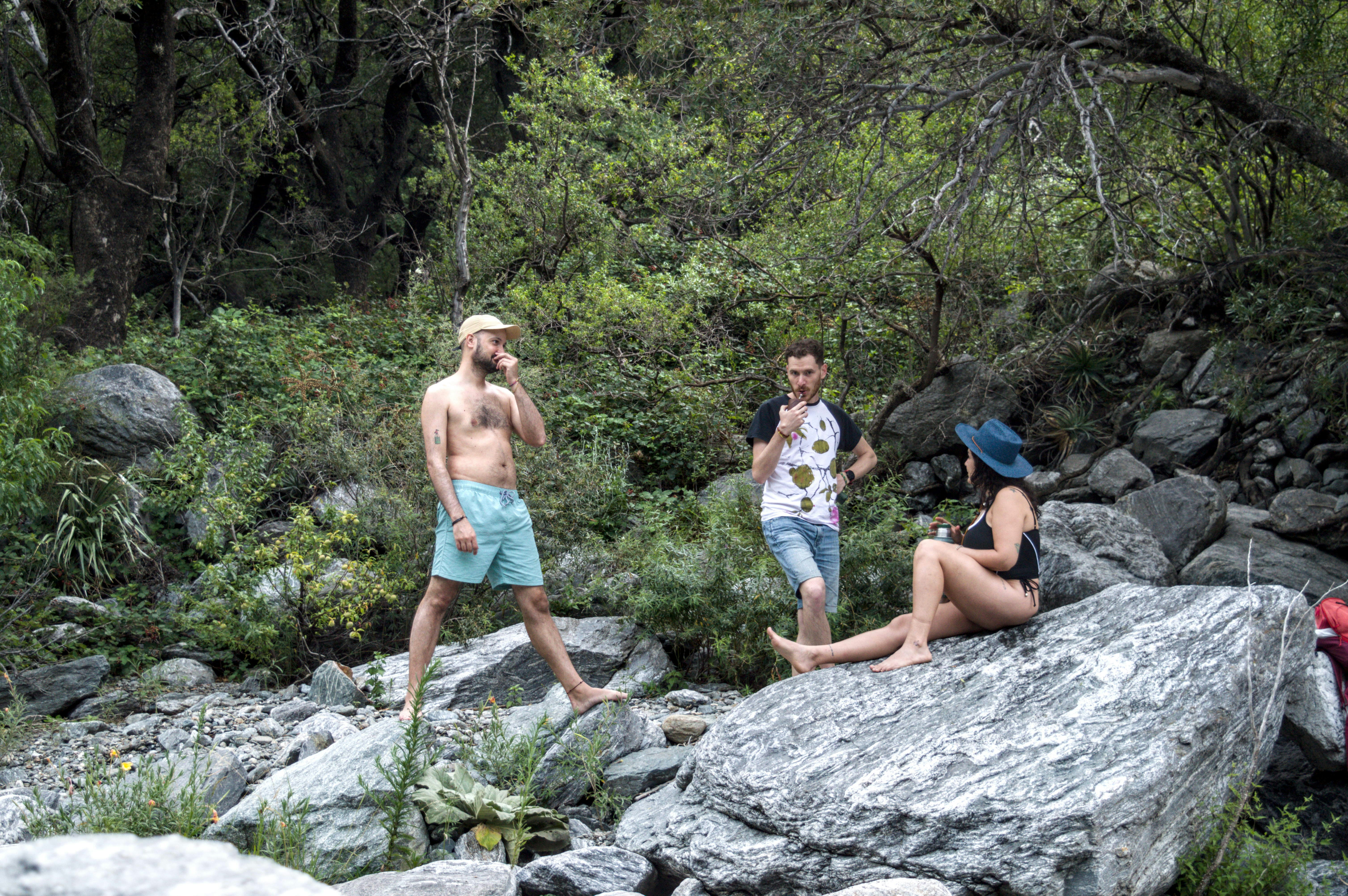 Sunlit camp by the river: three friends pause on a rocky shoreline