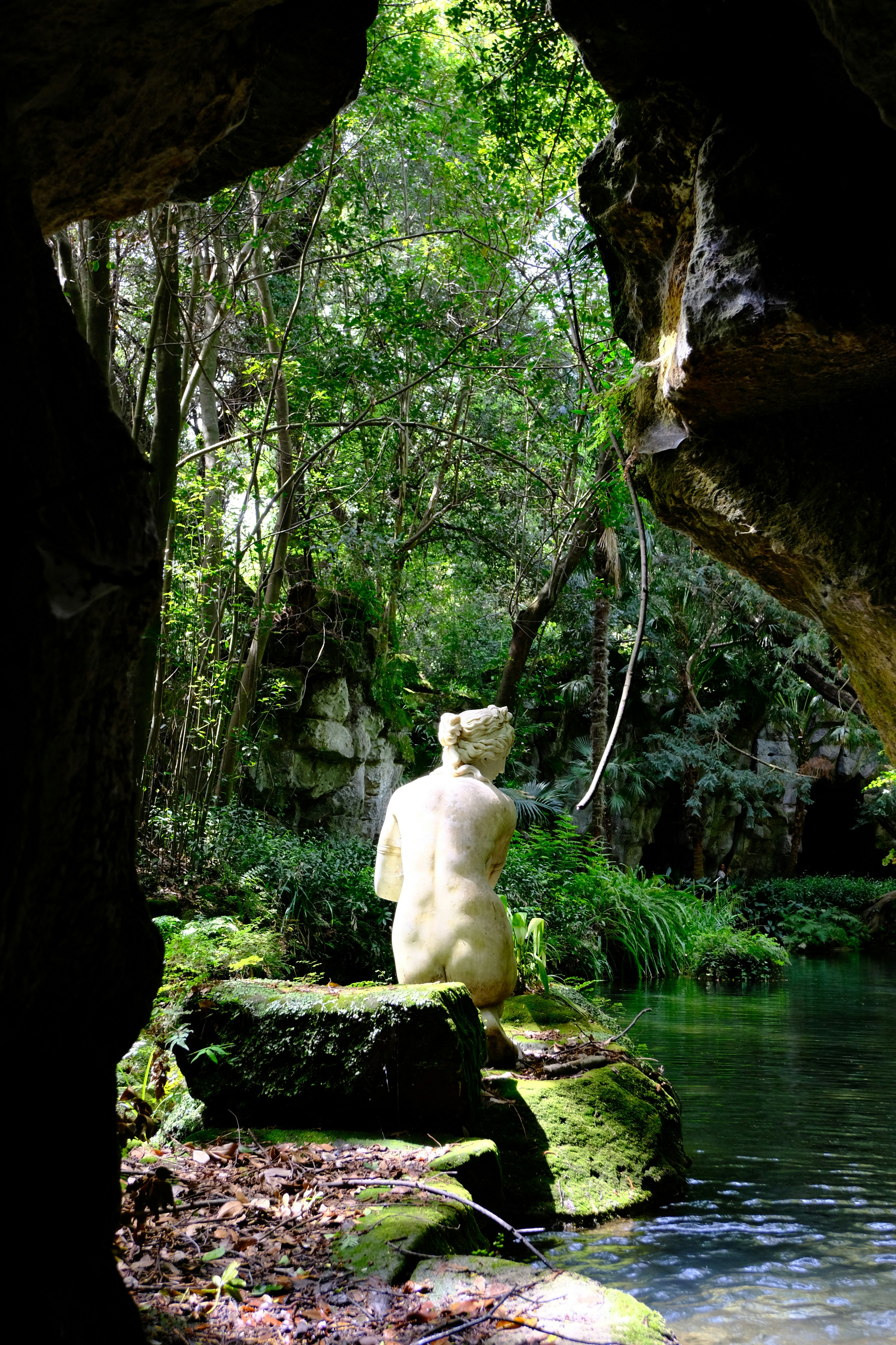Nude statue resting beside a mossy pool in a lush grotto