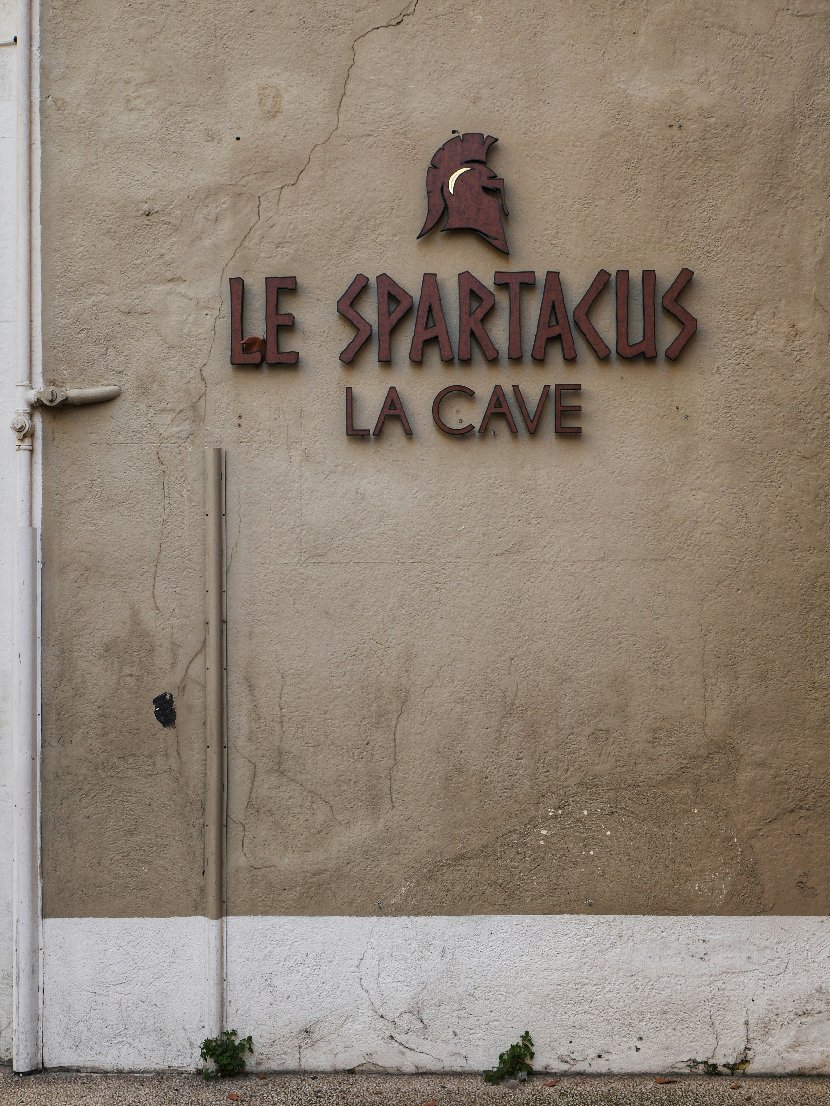 Le Spartakus La Cave: A Weathered Sign on Sunlit Stucco